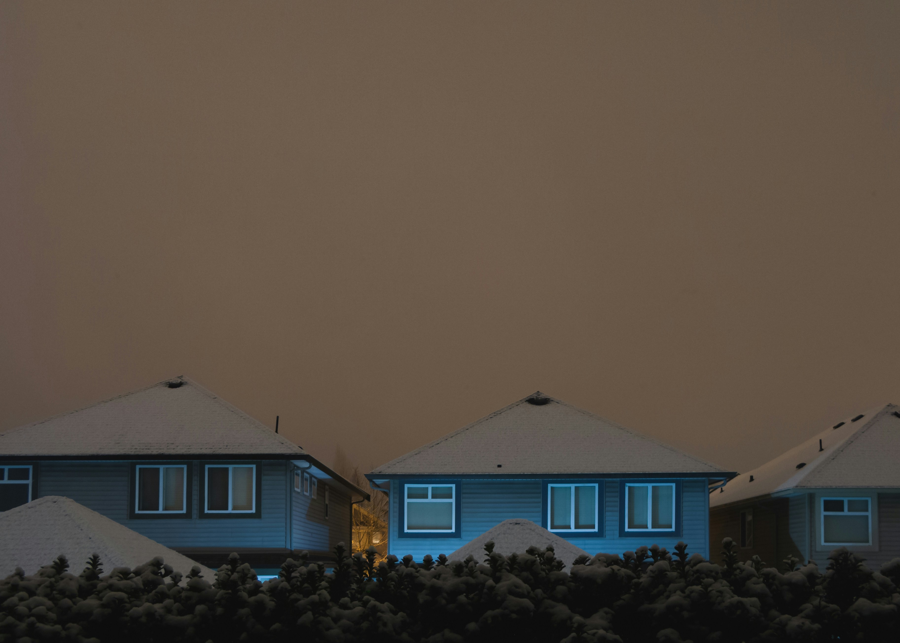 Snow-covered houses under a muted sky, illuminated by soft light from a nearby window.