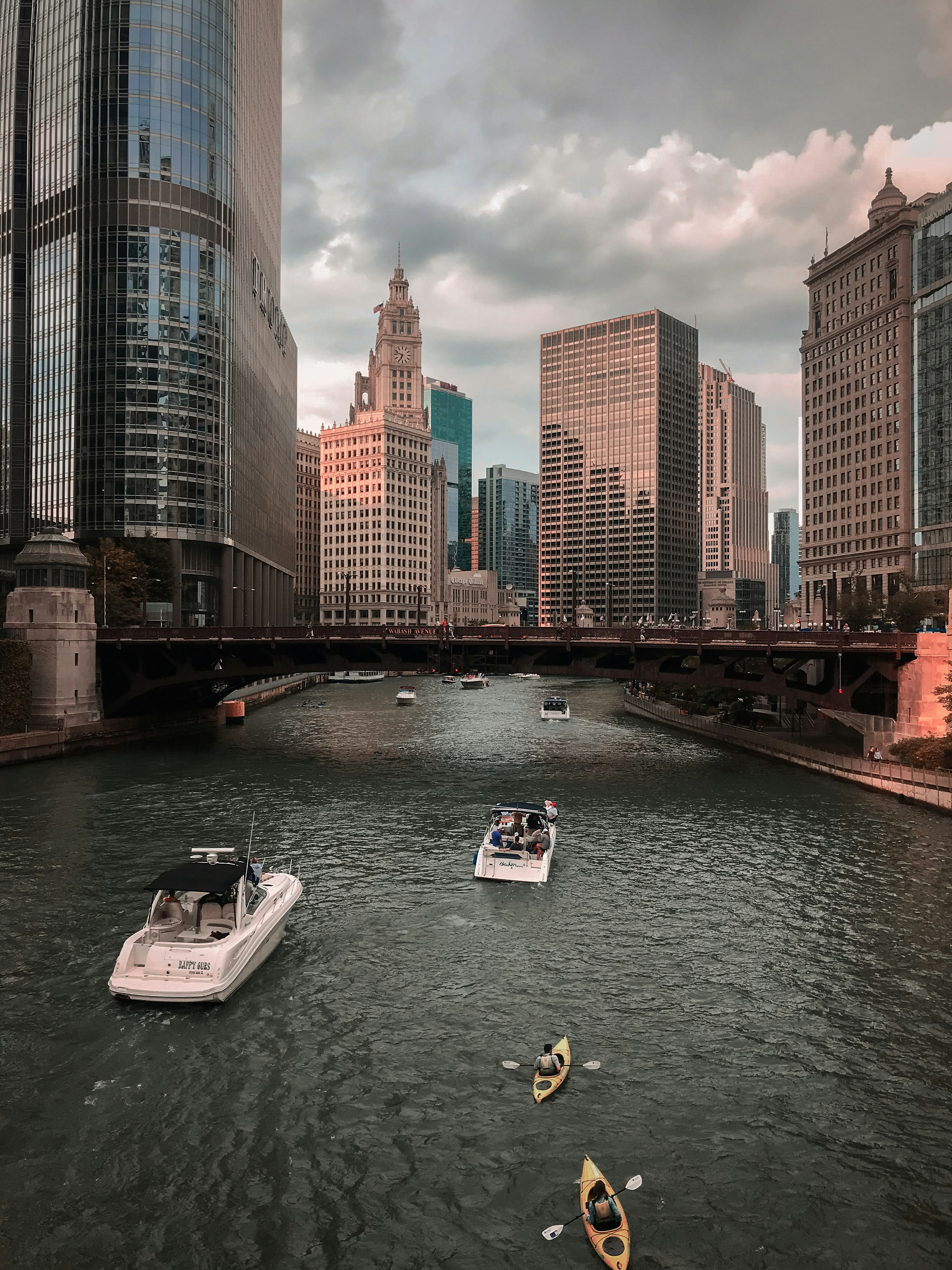 Boats and kayakers navigate a bustling river framed by towering skyscrapers in a vibrant cityscape.