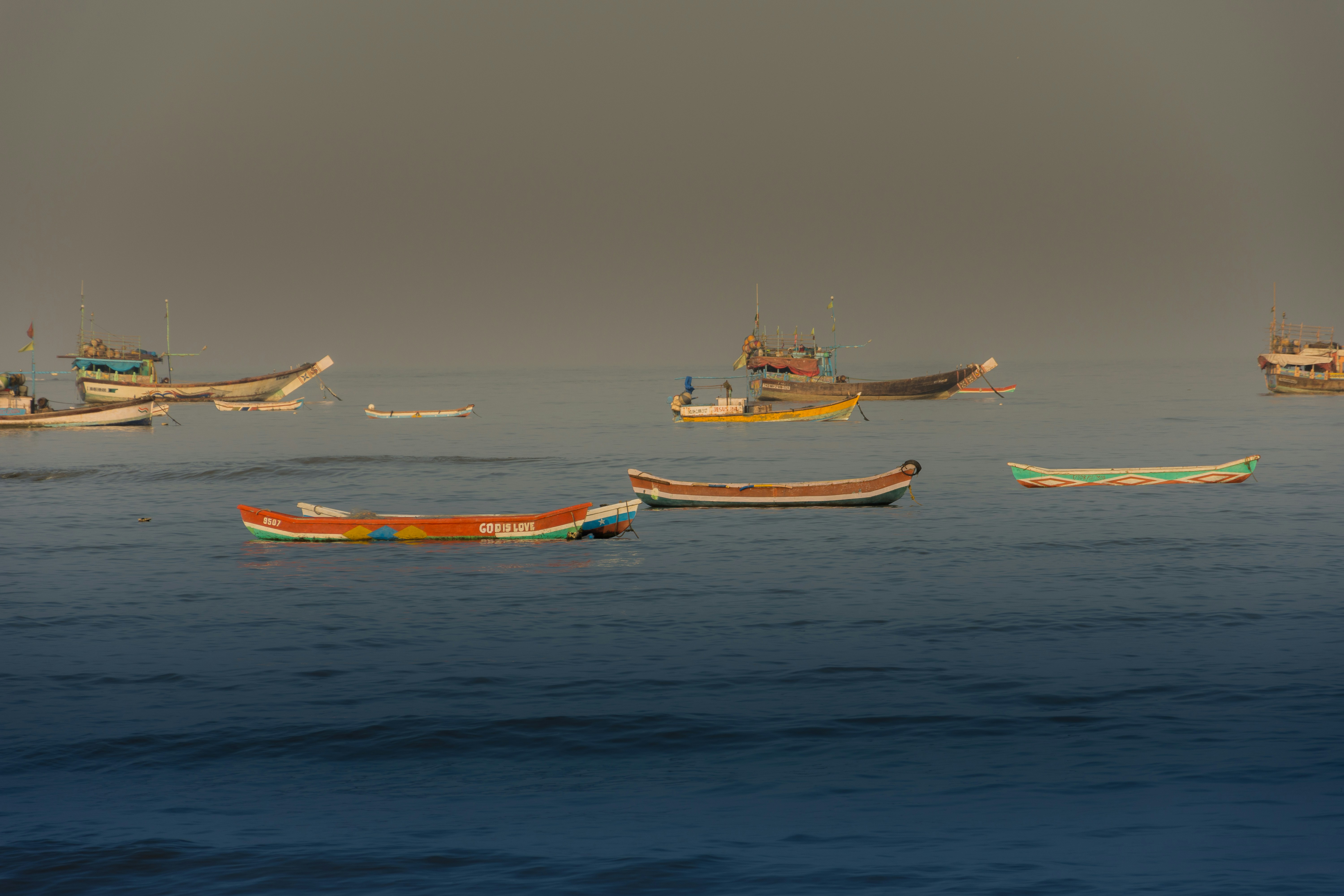 Fishing boats gently floating on a misty sea under a gray sky.