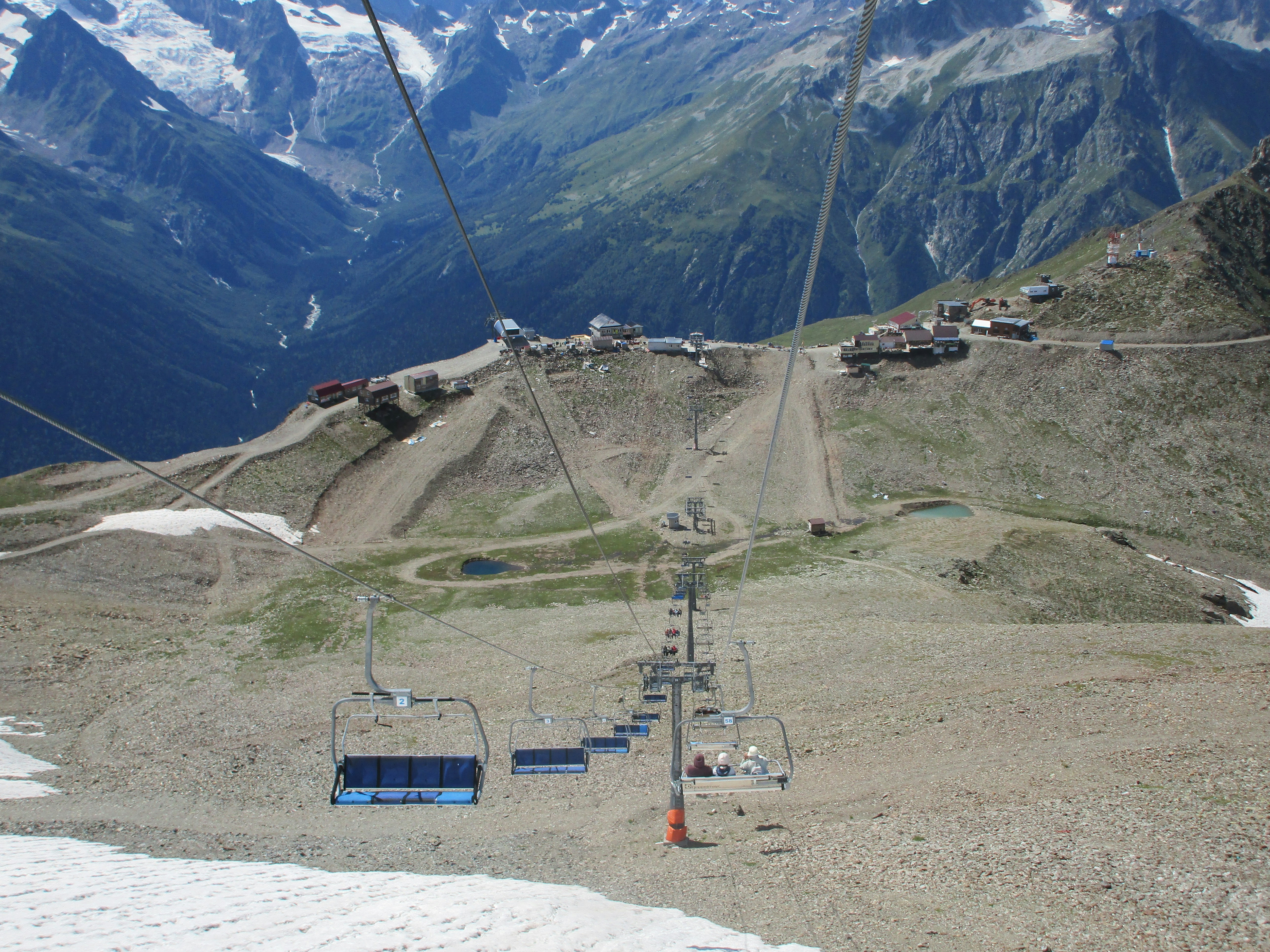 A chairlift descends over a rugged mountain landscape, showcasing the serene beauty of high-altitude terrain and ski facilities below.