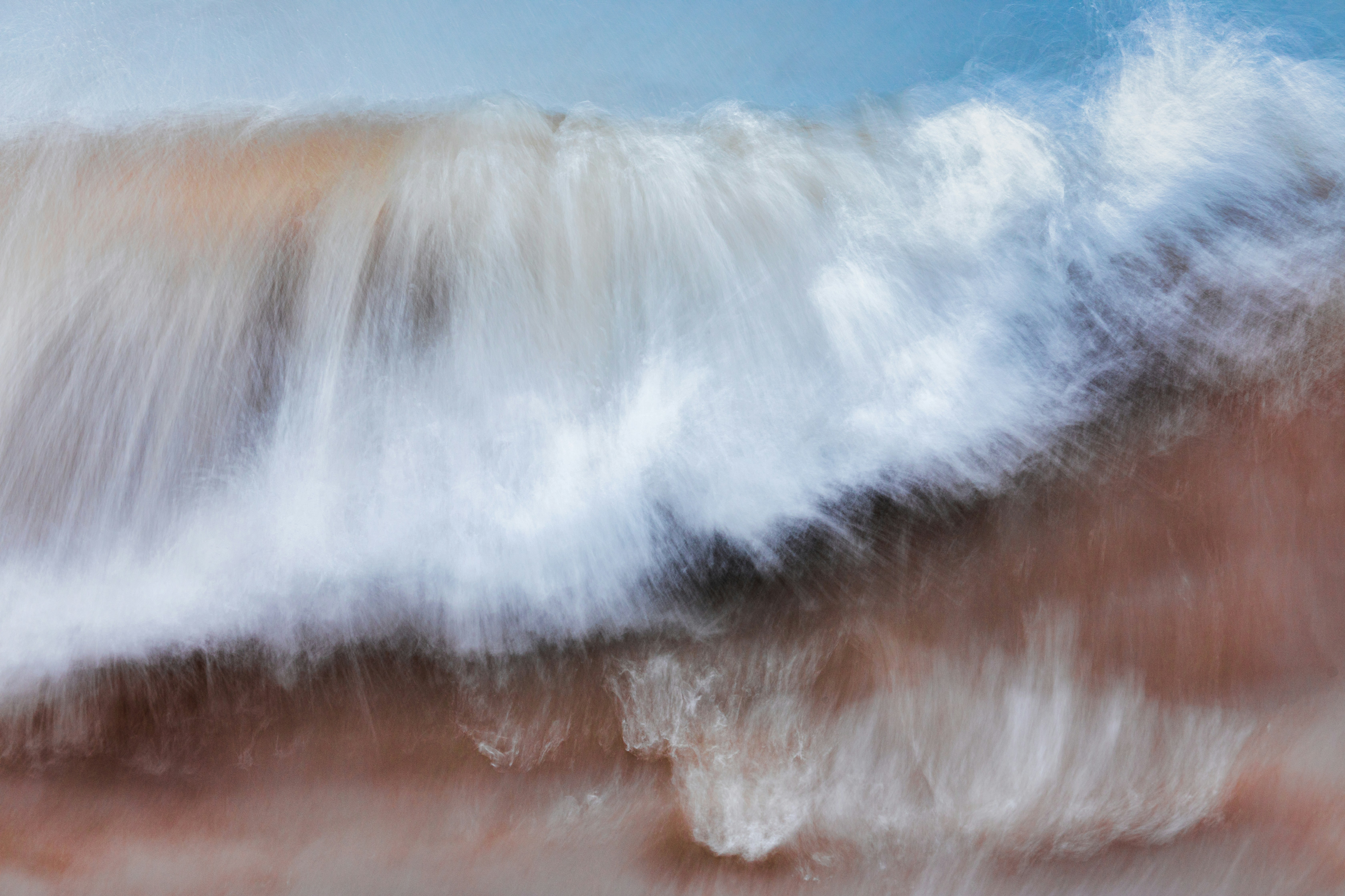 Dynamic ocean wave crashing against the shore, blending hues of blue and brown. The motion captures the essence of nature's rhythm.