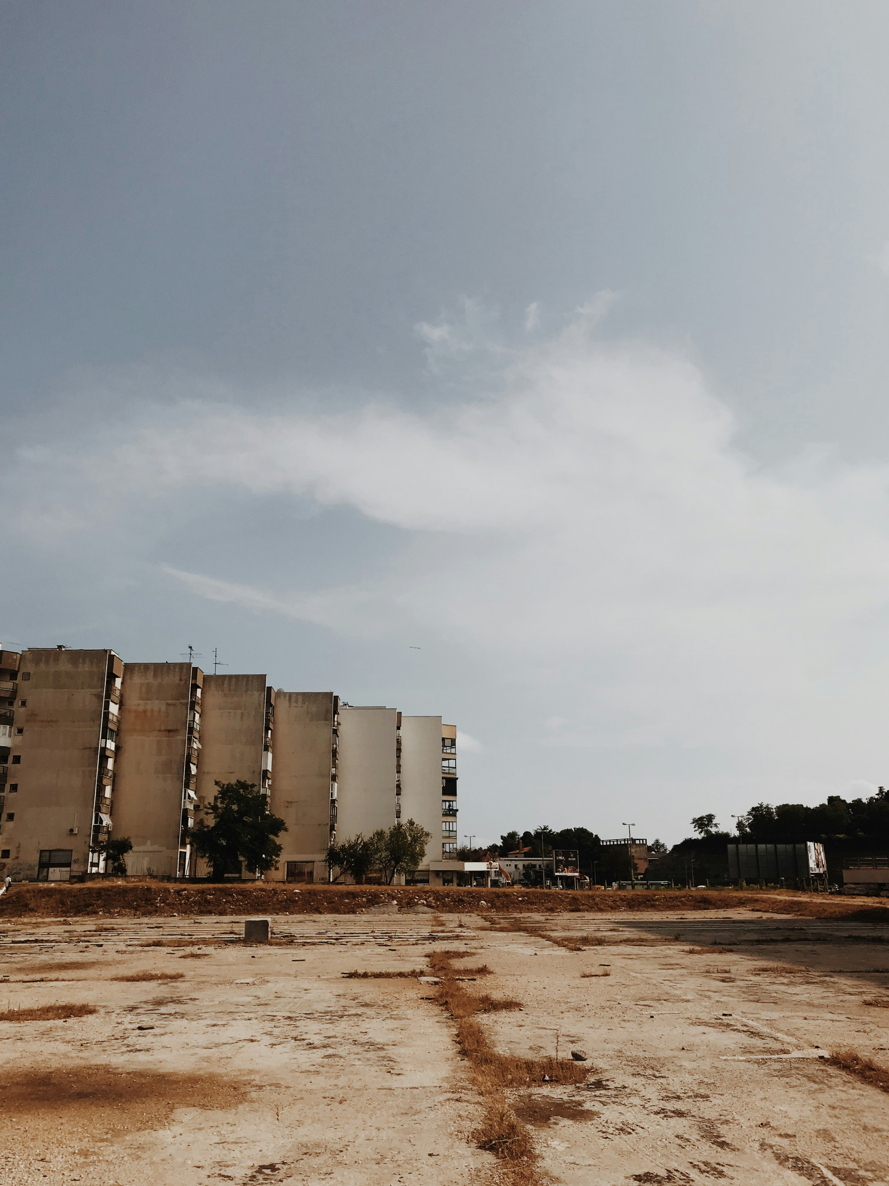 Desolate urban landscape featuring a row of weathered apartment buildings against a clear sky. Dry earth and sparse vegetation hint at a forgotten space.