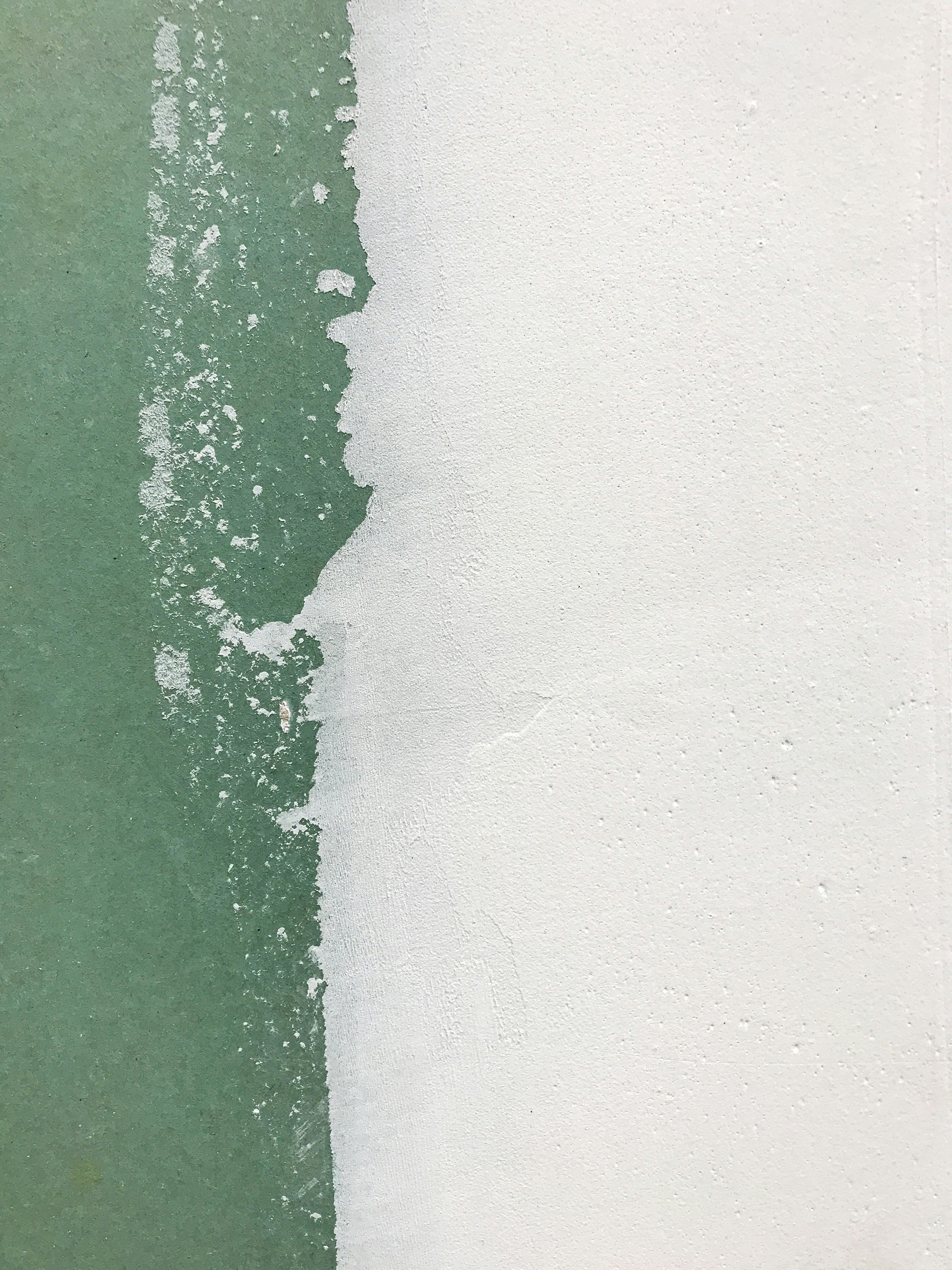 Close-up of a textured wall with a vertical division between green and white paint.