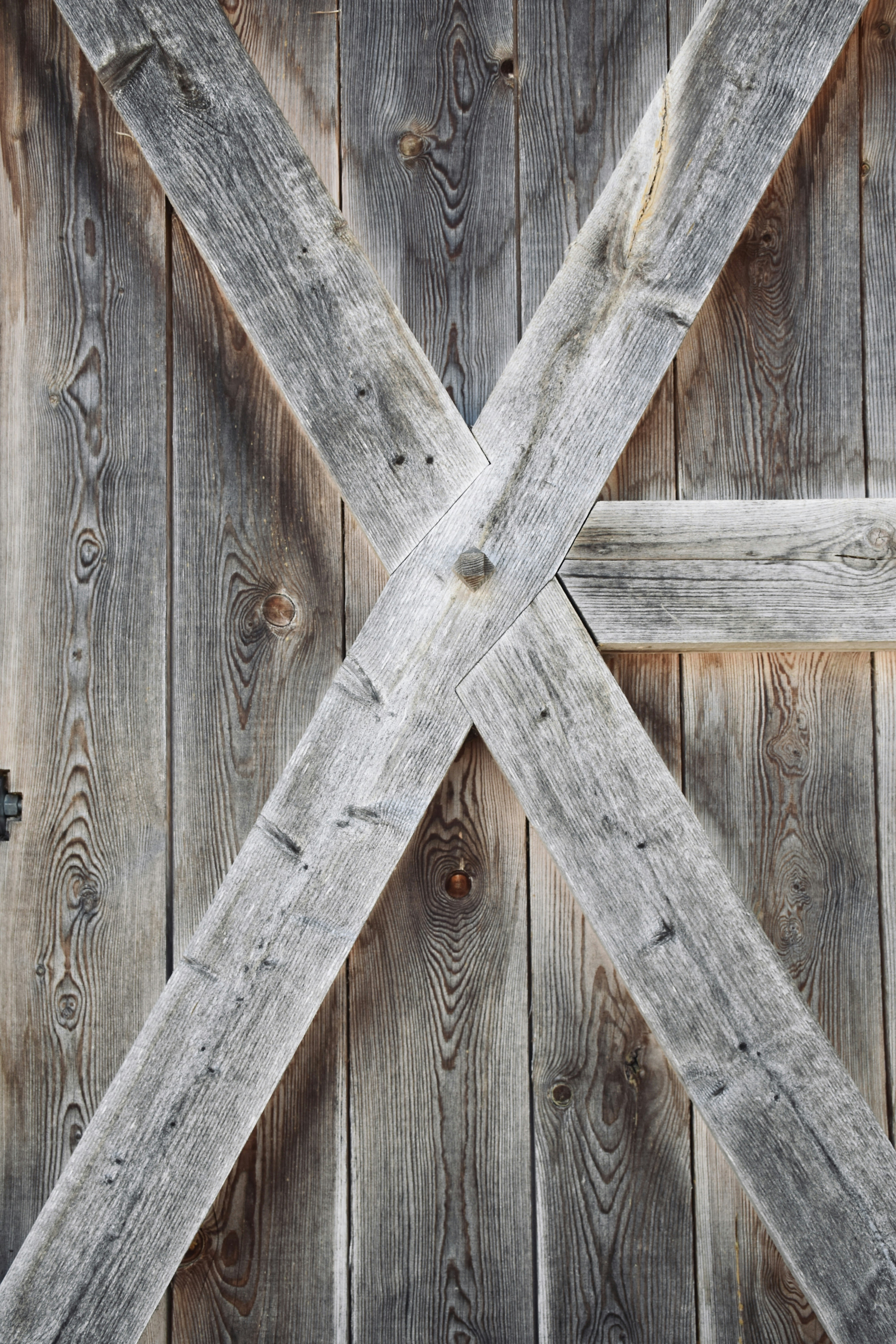 Weathered wooden barn door featuring an intricate X-brace design. The texture and grain of the wood add character and depth.
