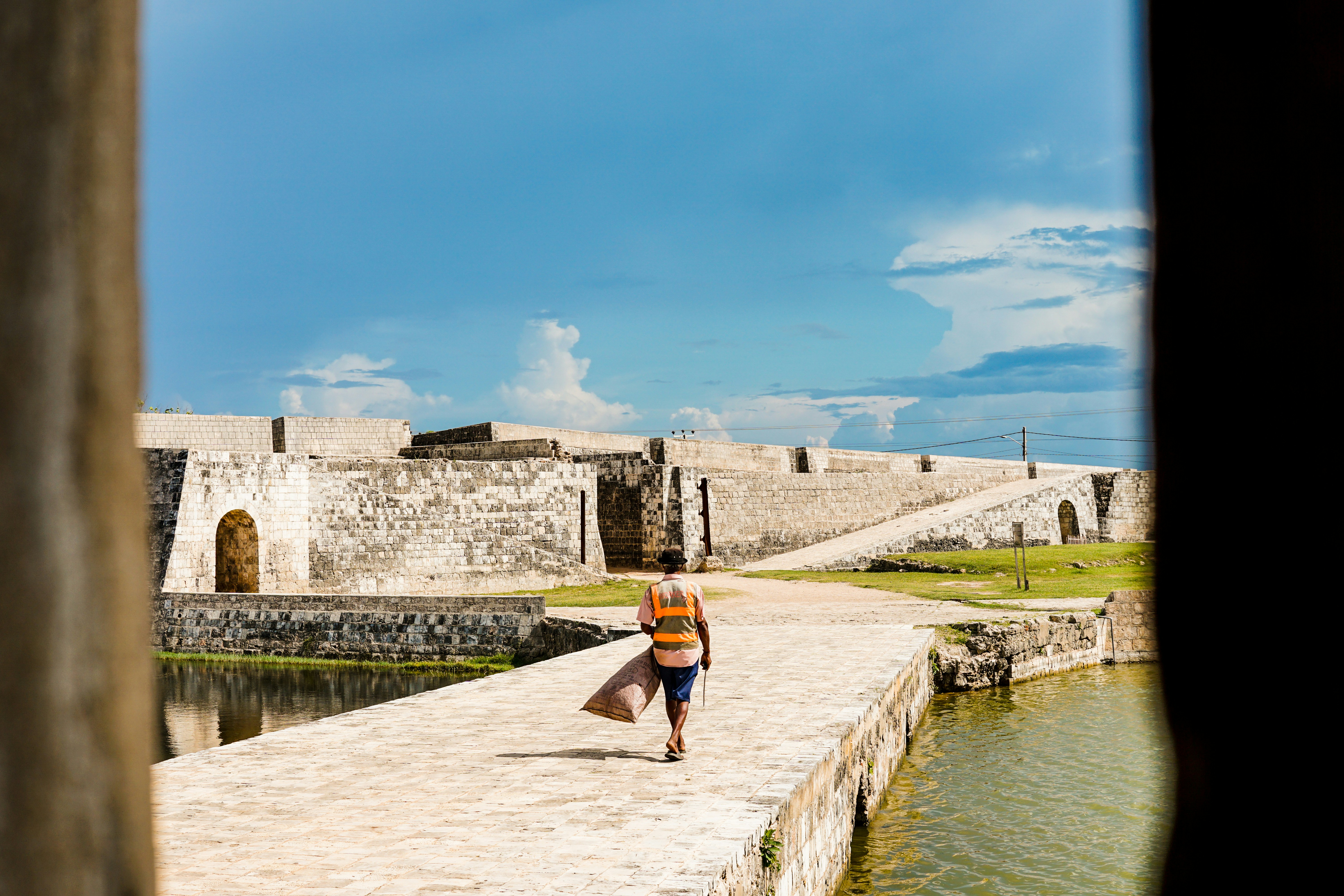 Person walking on a stone pier bordered by historic walls under a clear blue sky.