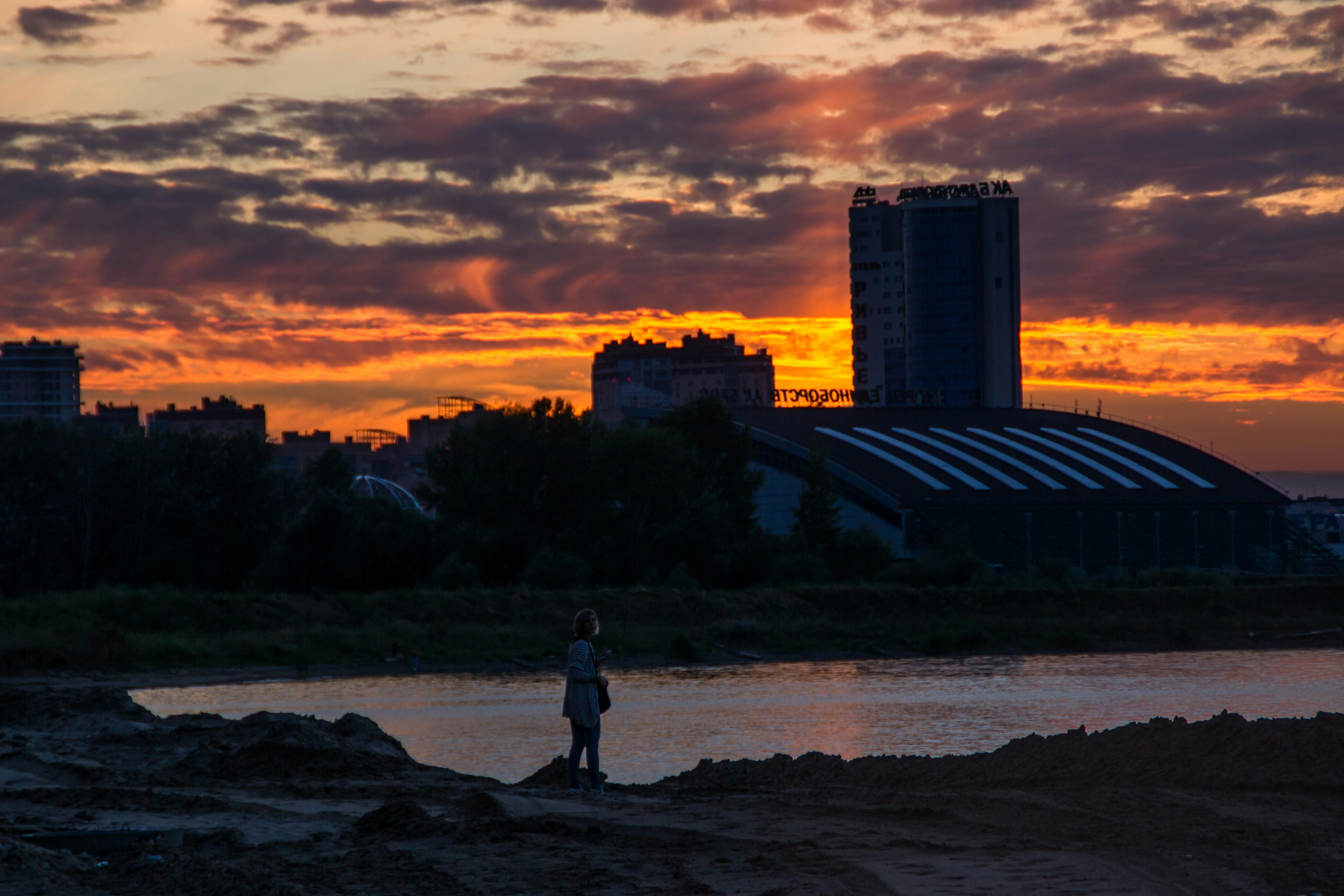 Dusk by the River: A solitary silhouette against an industrial skyline