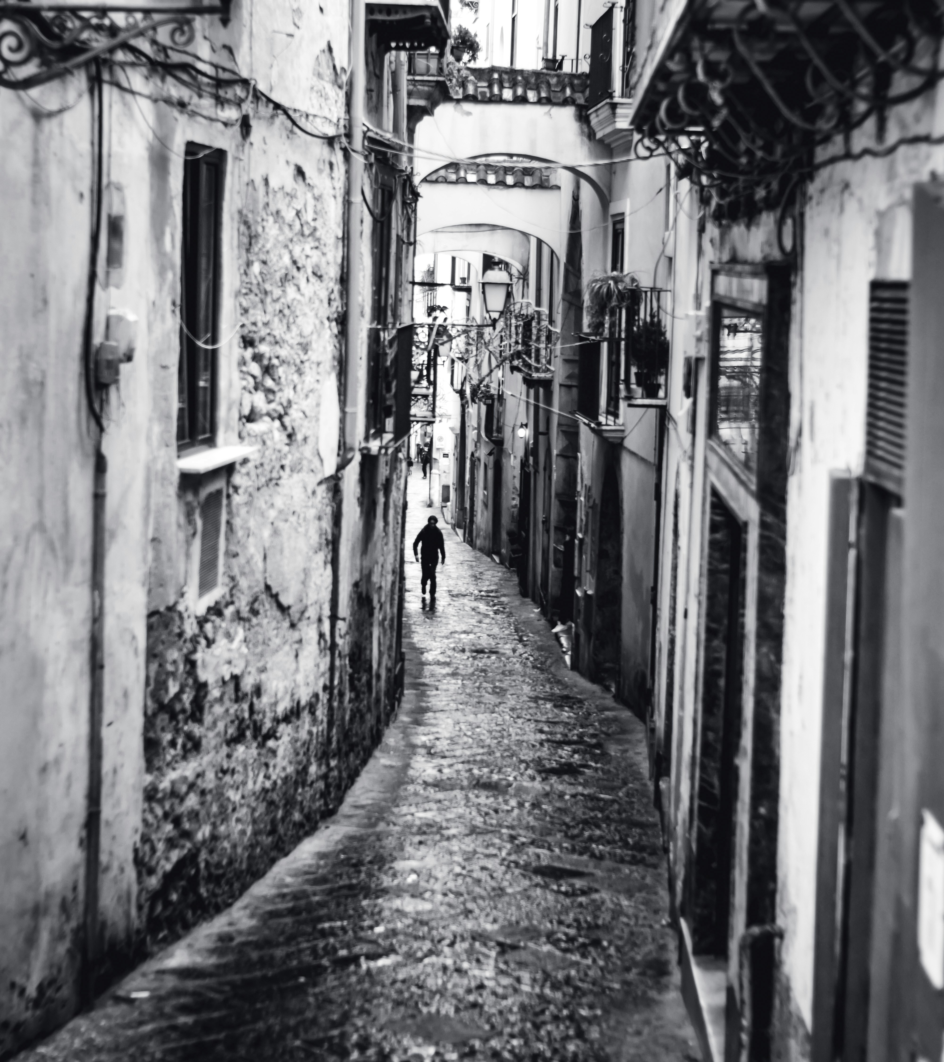 Grayscale photography of man walking on pathway surrounded by building ...