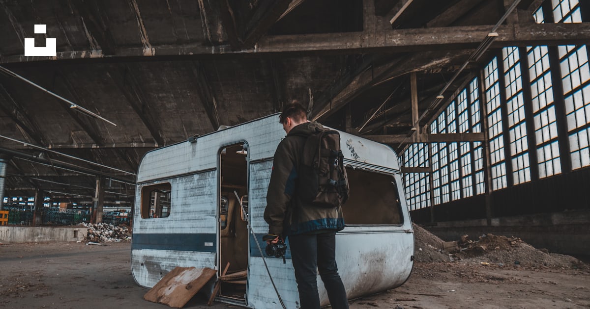 Man standing beside abandoned camper trailer inside building photo ... Man standing beside abandoned camper trailer inside building photo ...