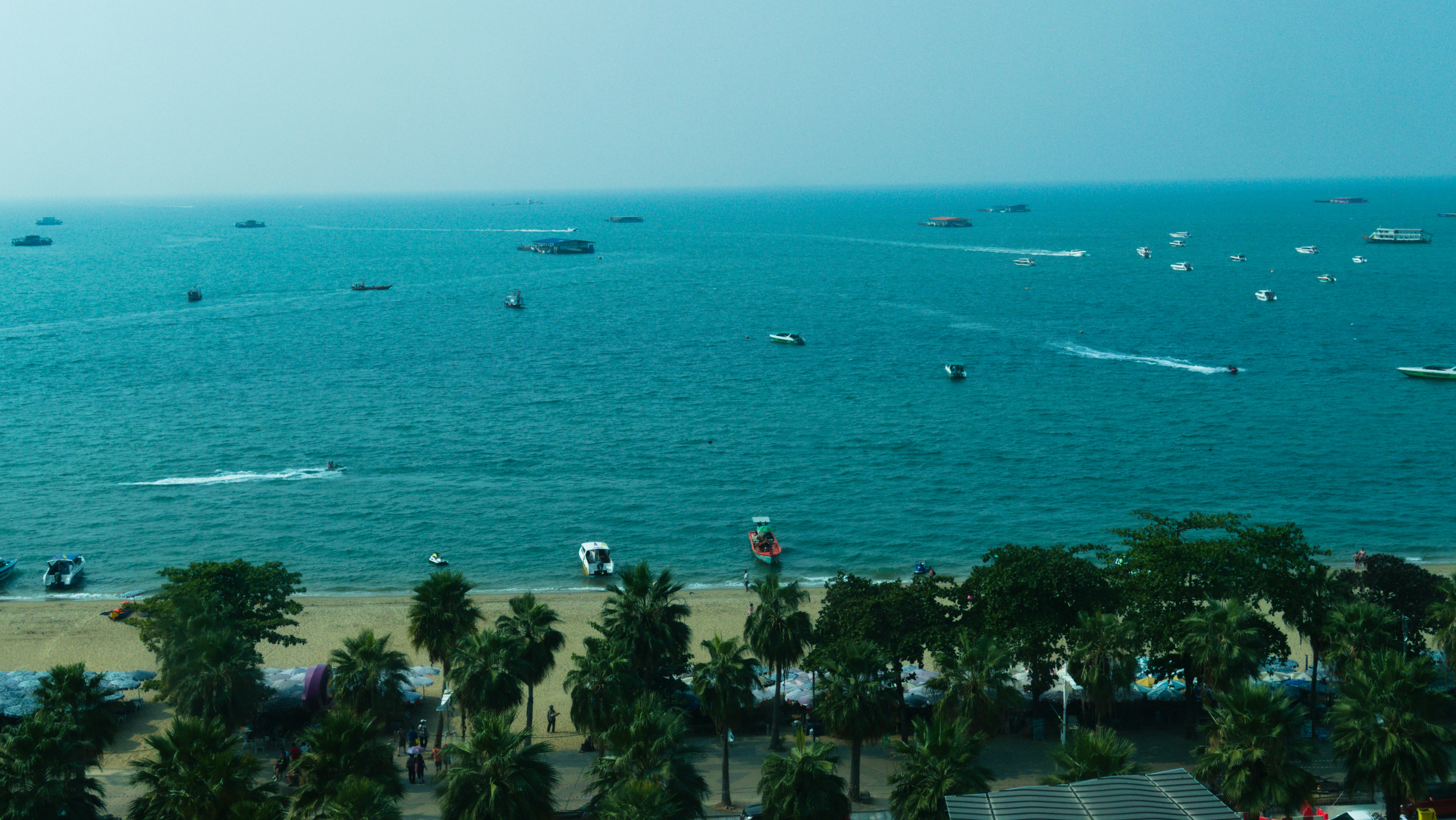 Aerial view of Pattaya's beach with boats scattered across the turquoise sea under a clear sky.