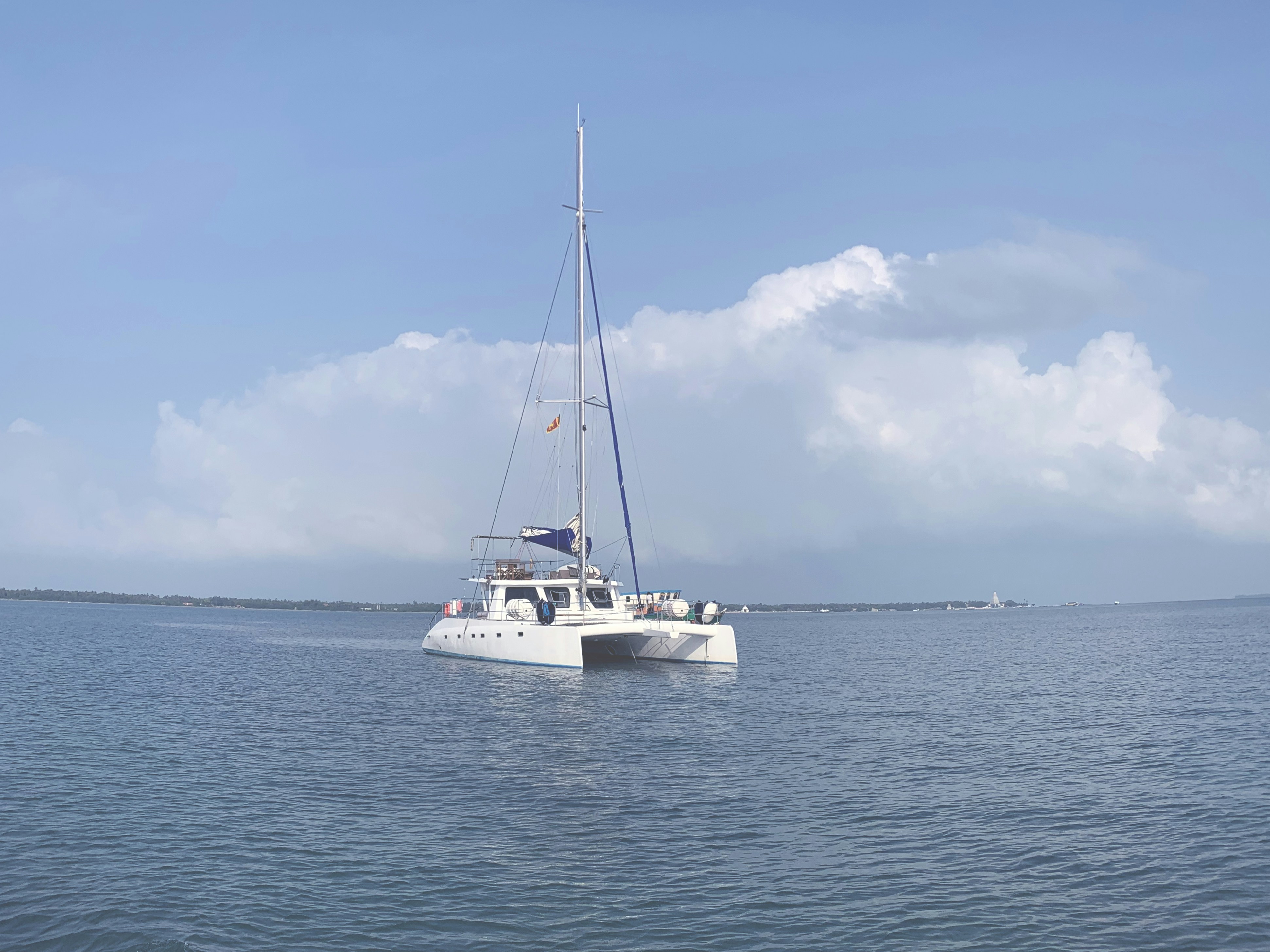 A sleek catamaran gliding through calm waters under a clear sky, framed by distant clouds. The scene captures the essence of peaceful sailing.