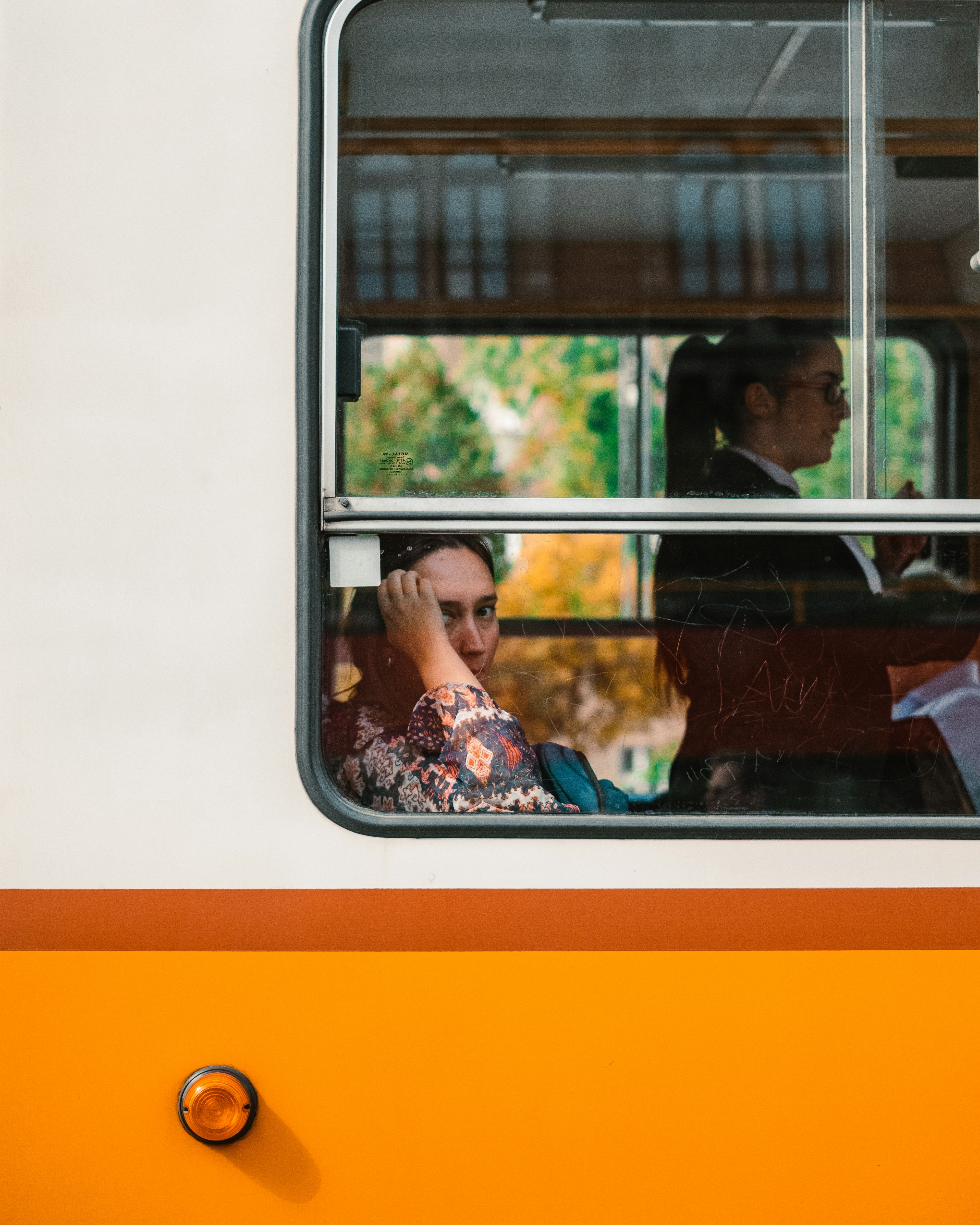 A woman gazes pensively through a bus window, lost in thought amidst the vibrant urban backdrop.