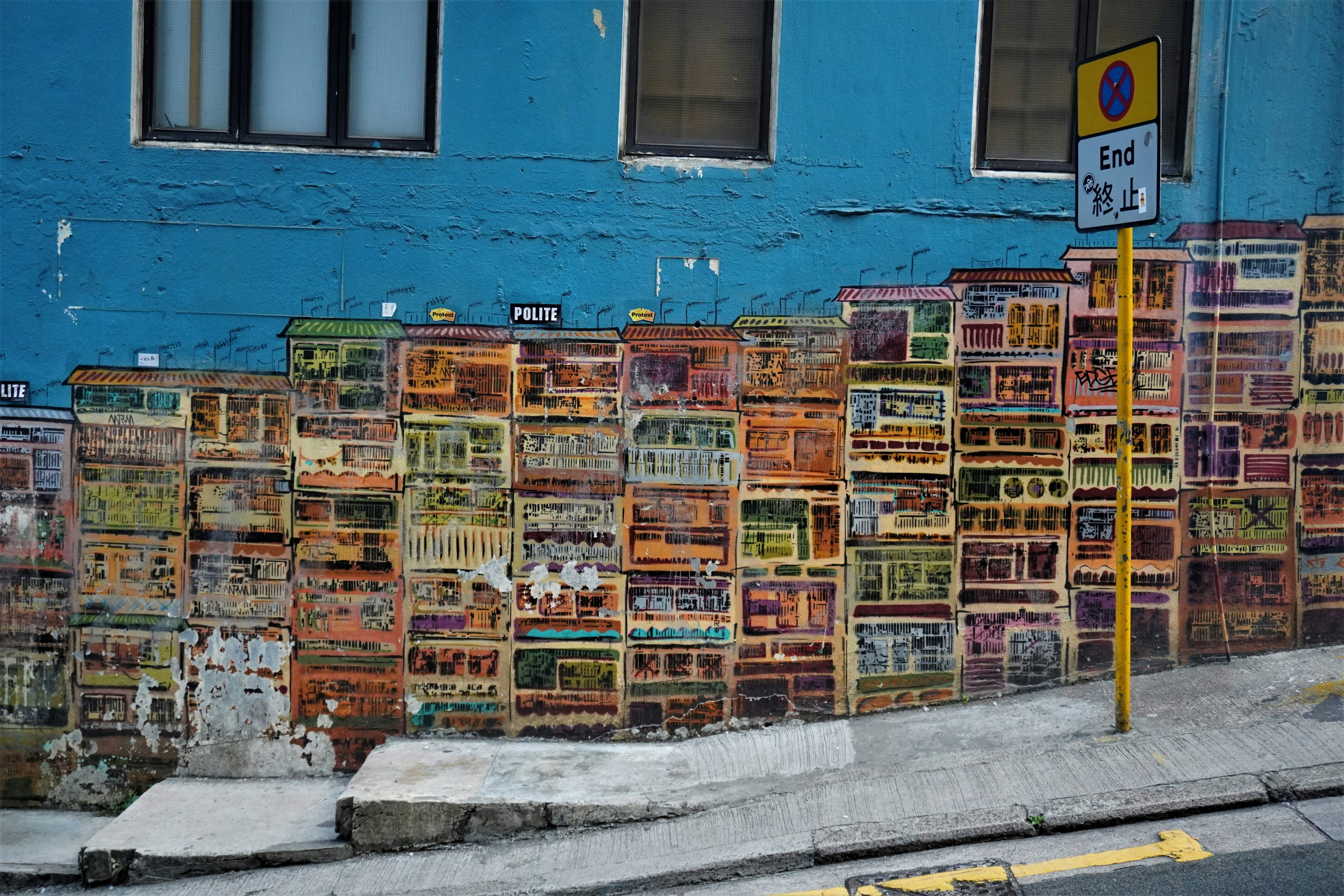 Colorful stacked crates form a vibrant mural against a blue wall on a sloped street.