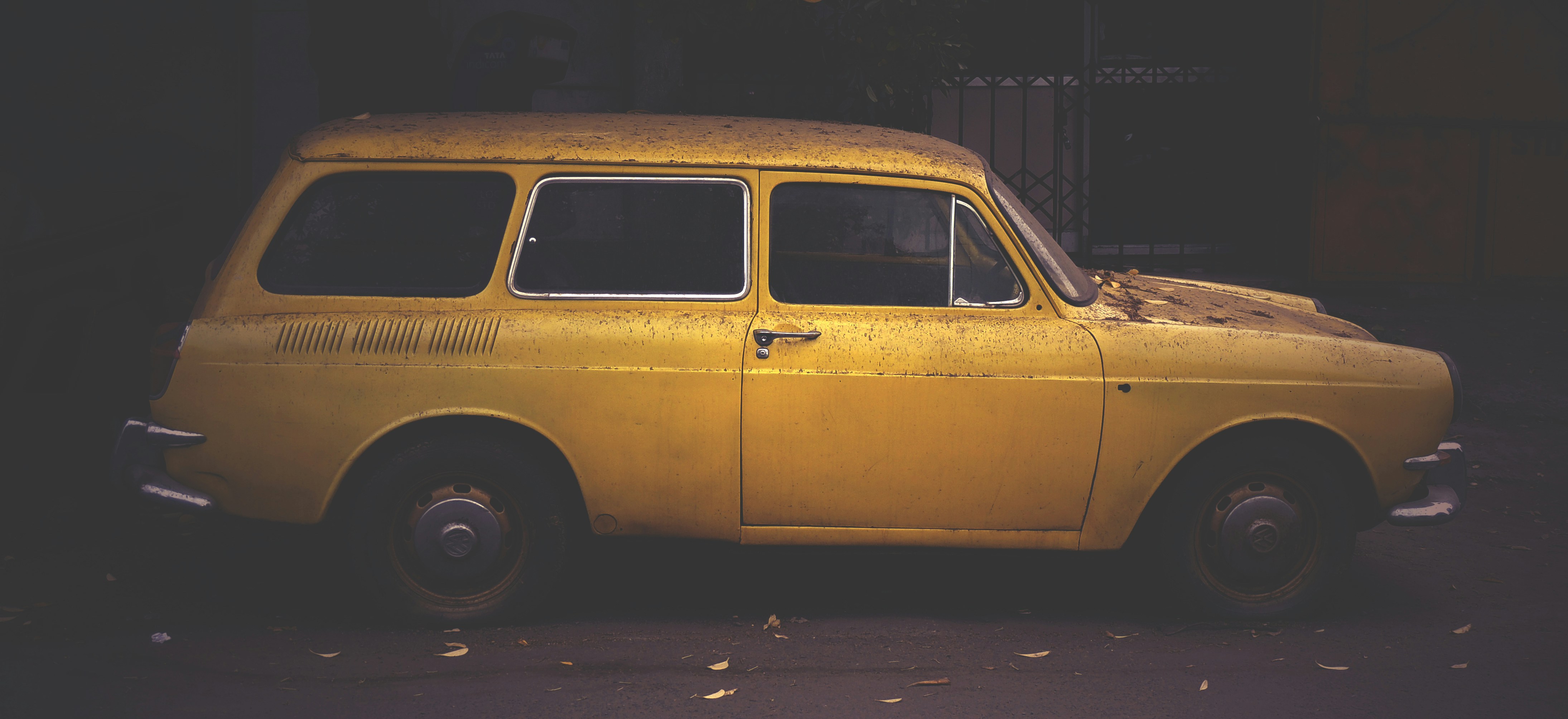 A weathered yellow station wagon parked in a dimly lit street, showcasing its retro charm and signs of age.