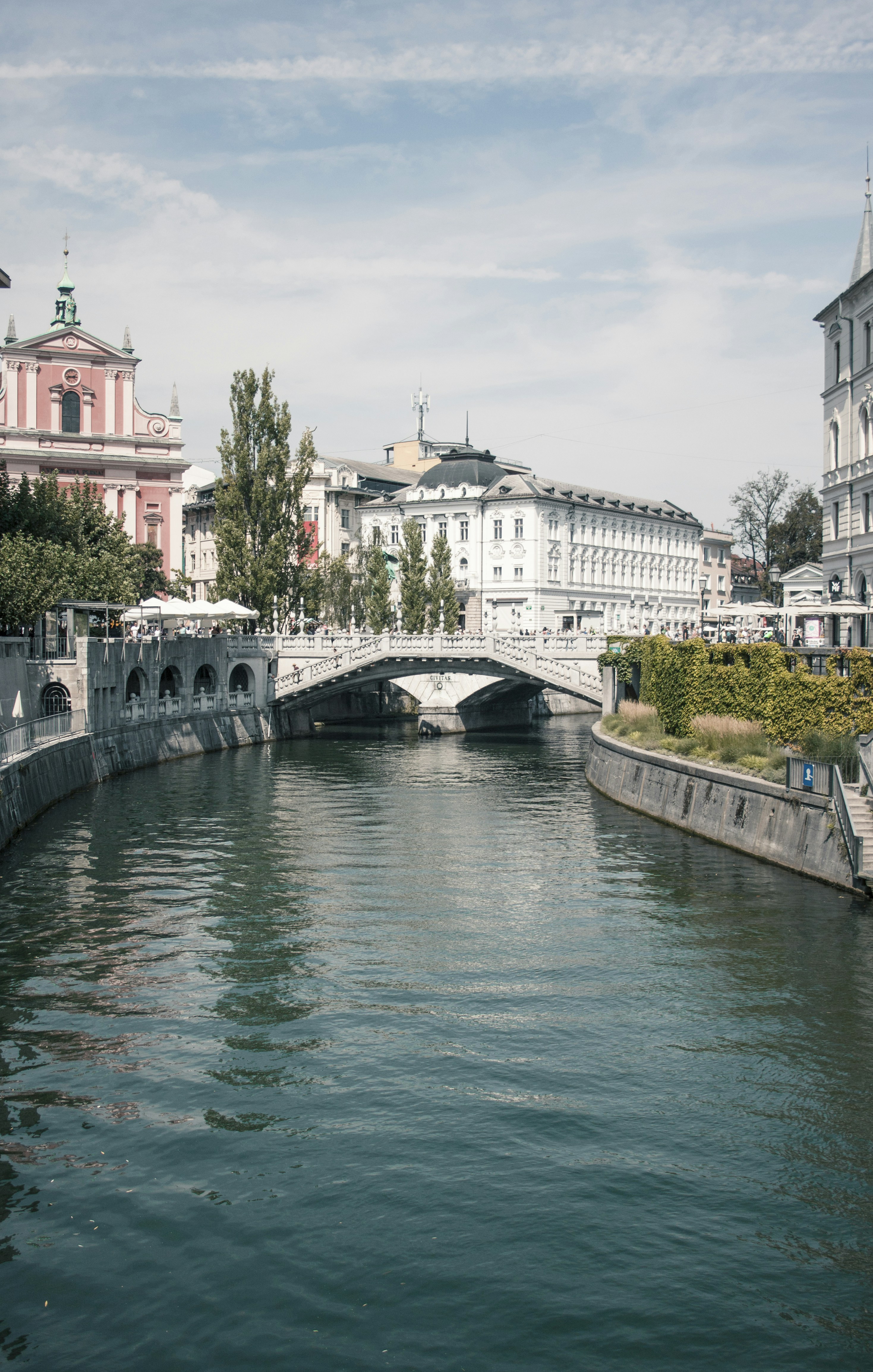 Charming canal scene in Ljubljana showcasing a historic bridge and elegant architecture along the water's edge.