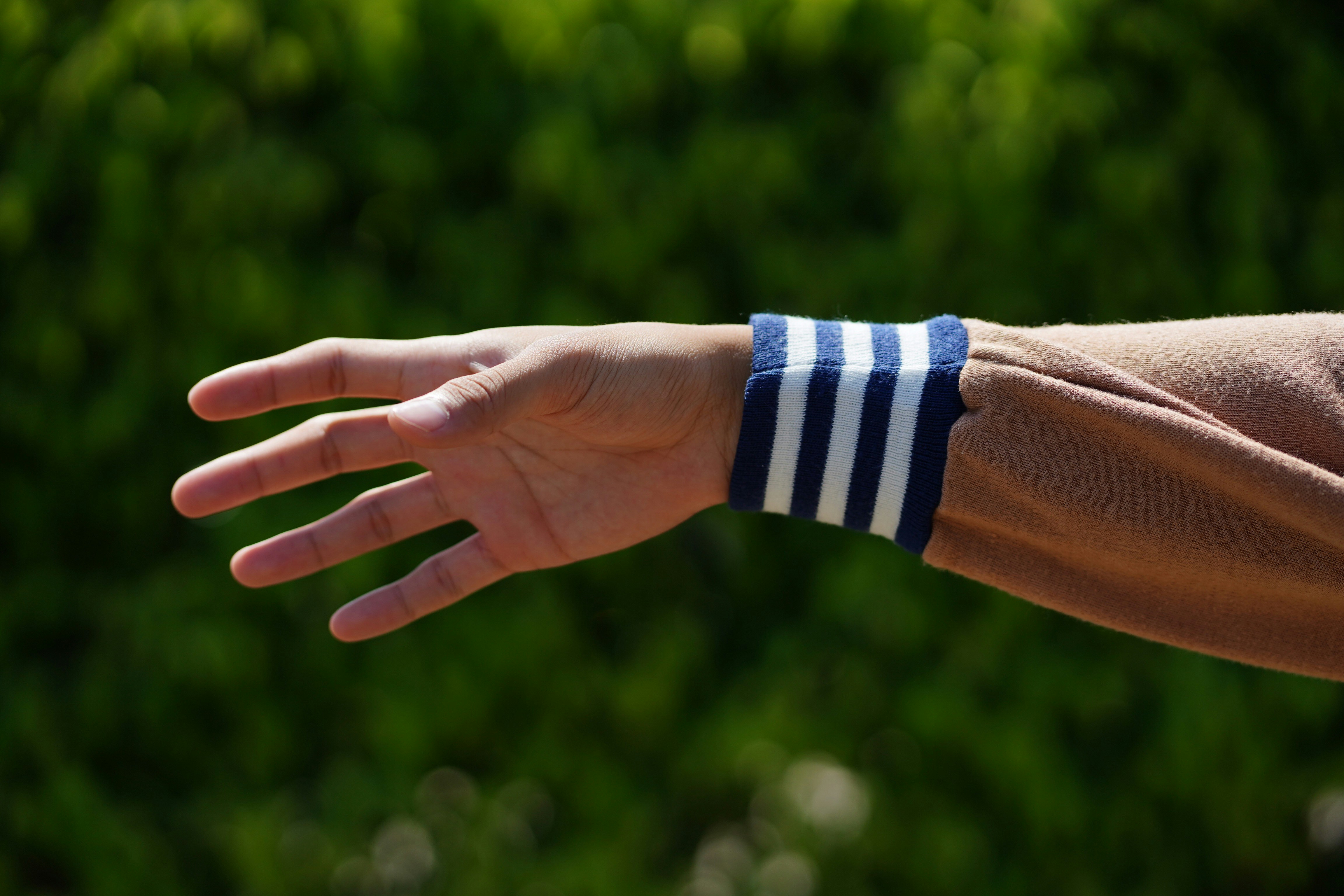 Outstretched hand adorned with a striped cuff against a lush green backdrop.