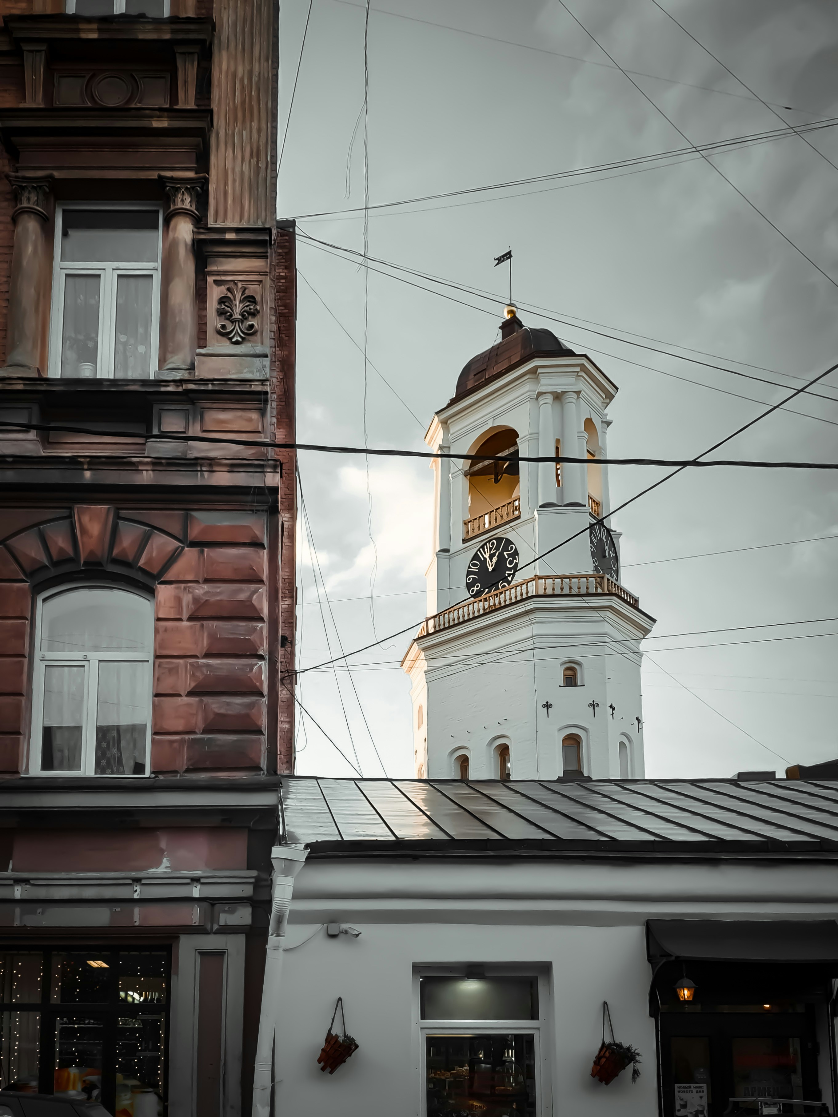 White clock tower rises beside a red-brick building, with overhead wires crisscrossing the urban scene.