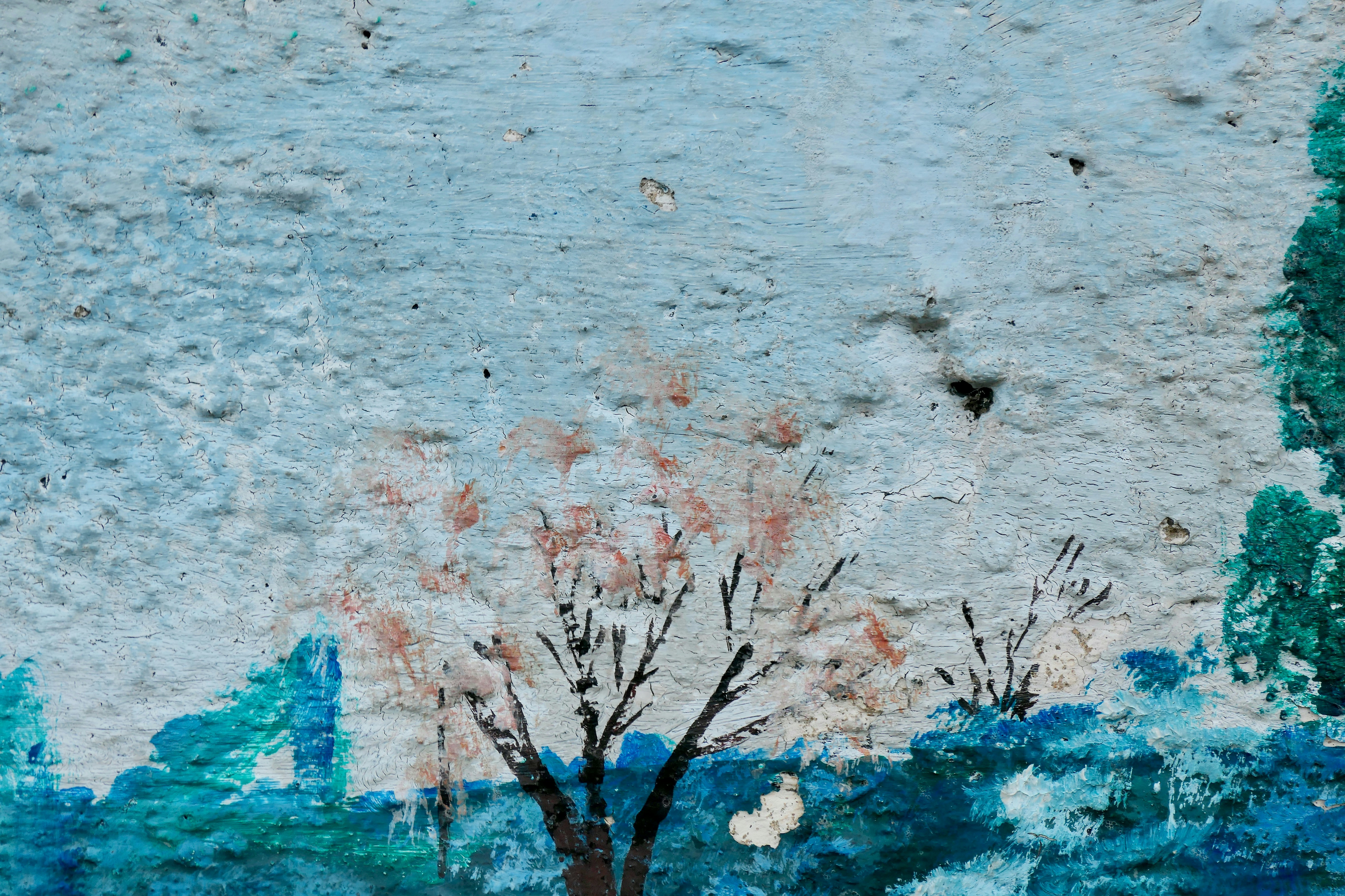 Faded mural depicting a tree against a textured blue background, showcasing the passage of time and nature's resilience.
