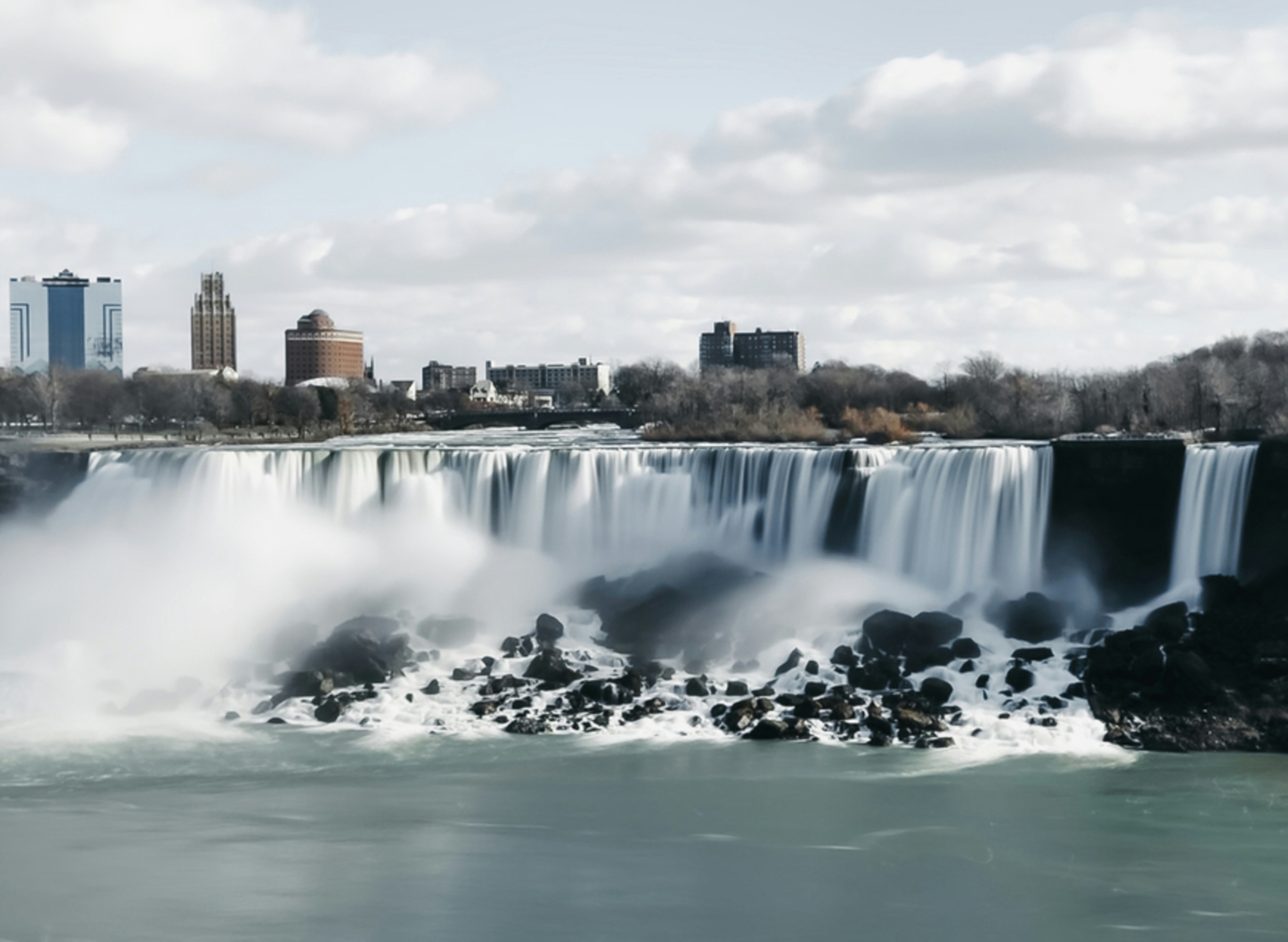 Majestic waterfalls cascading into a misty embrace, framed by an urban skyline in the distance.