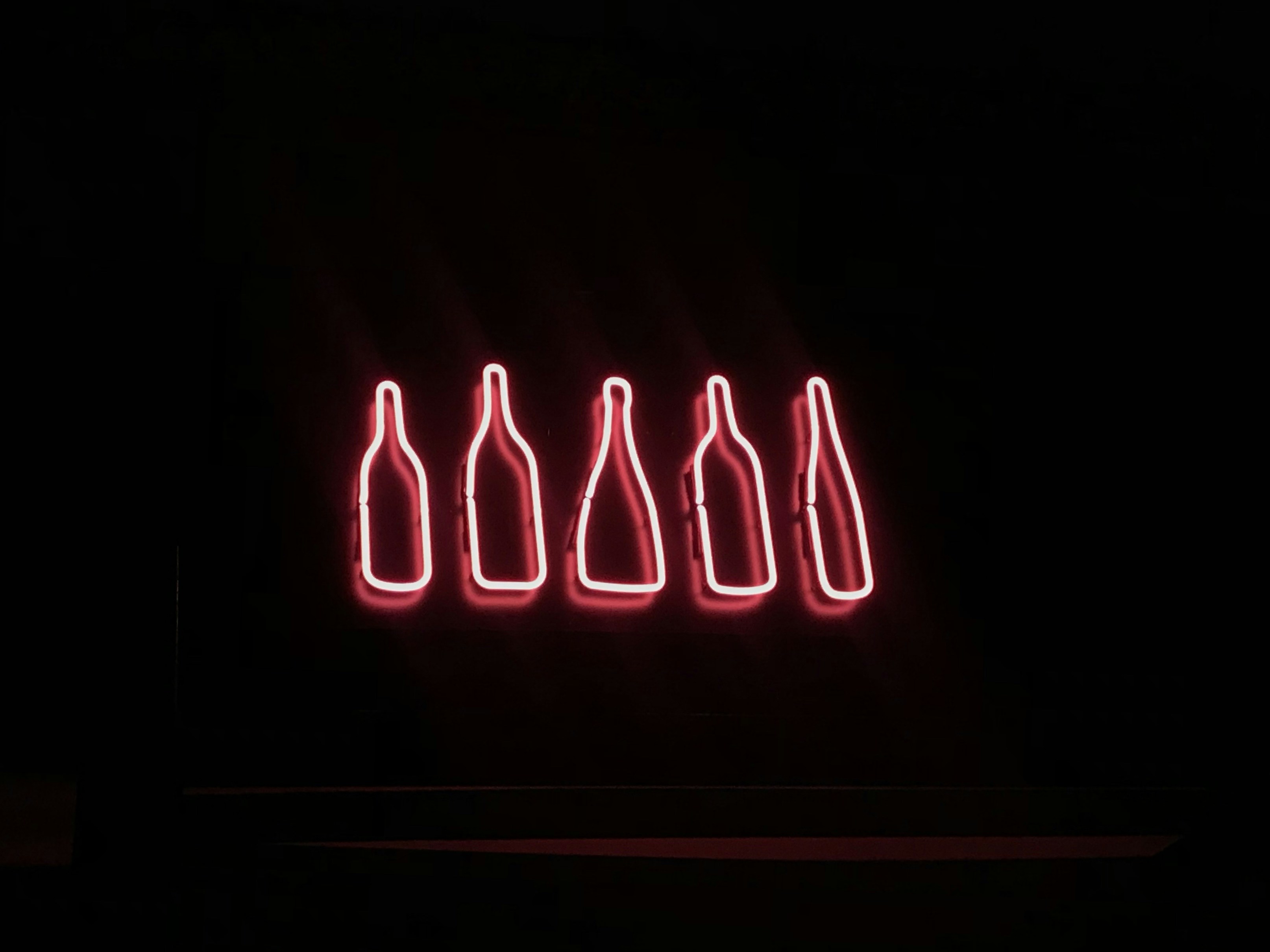 Neon Bottles: A Row of Red Glass Shadows in the Dark