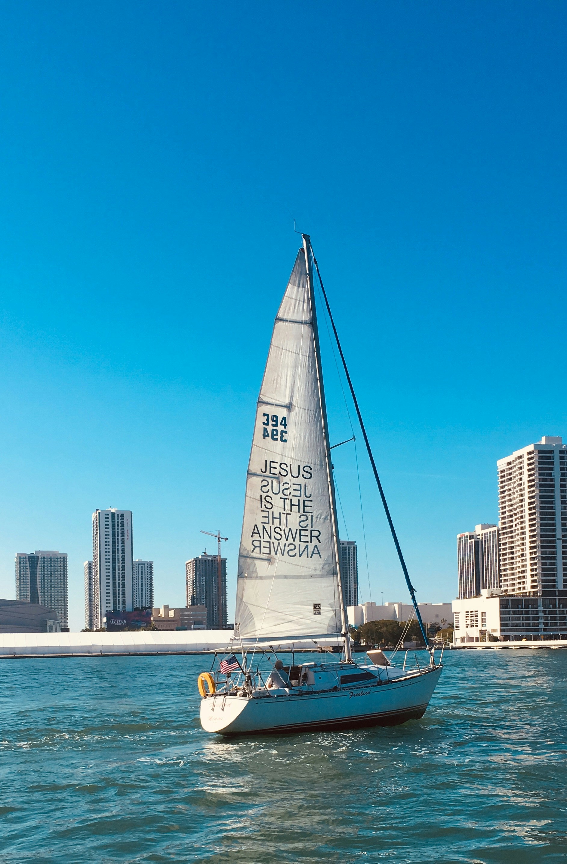Azure Harbor Sail: A lone vessel threading the city’s blue horizon