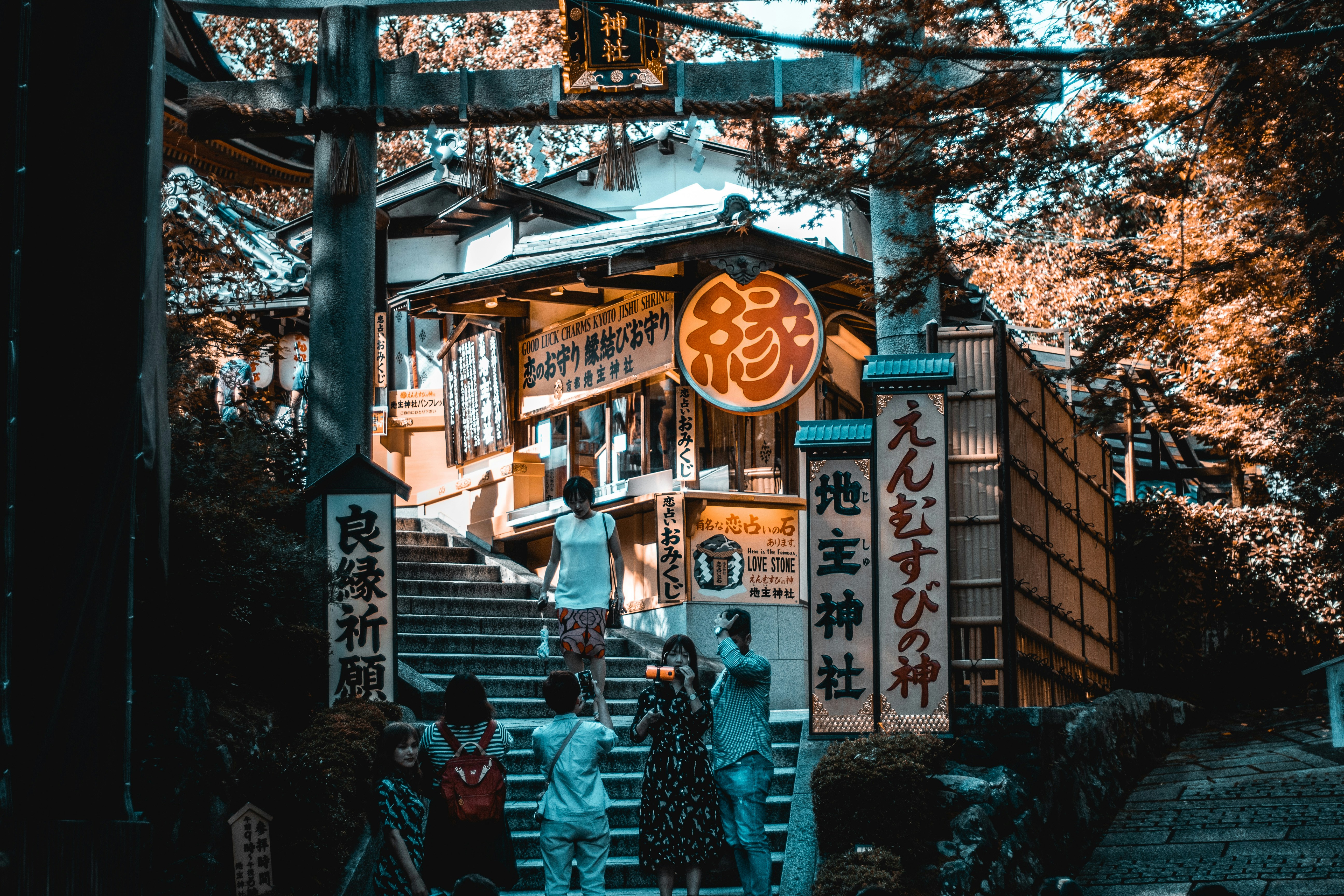 Visitors ascending the steps of a traditional shrine, surrounded by vibrant signage and lush greenery.