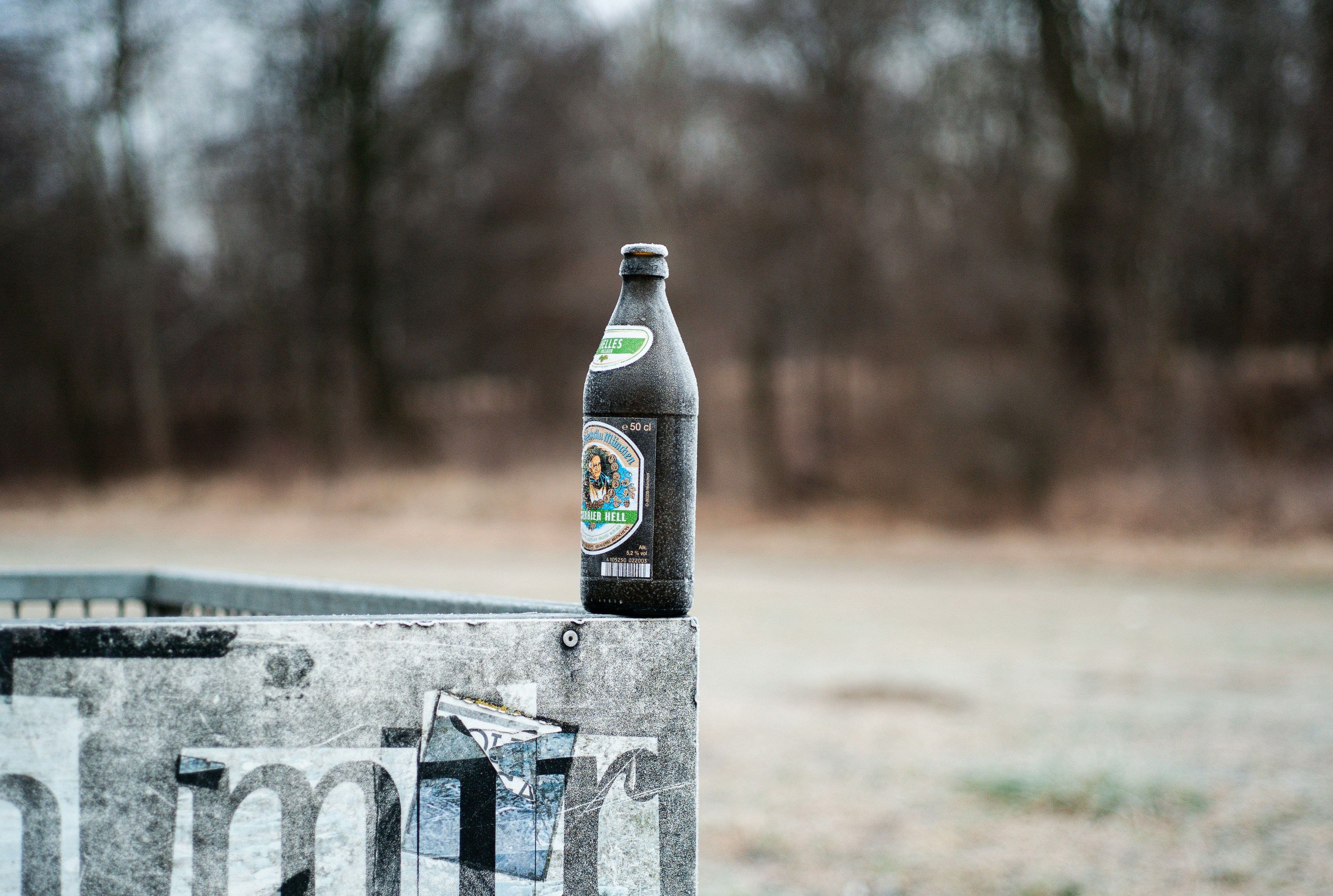 A solitary bottle rests on a weathered sign, surrounded by a muted landscape, evoking a sense of nostalgia and abandonment.