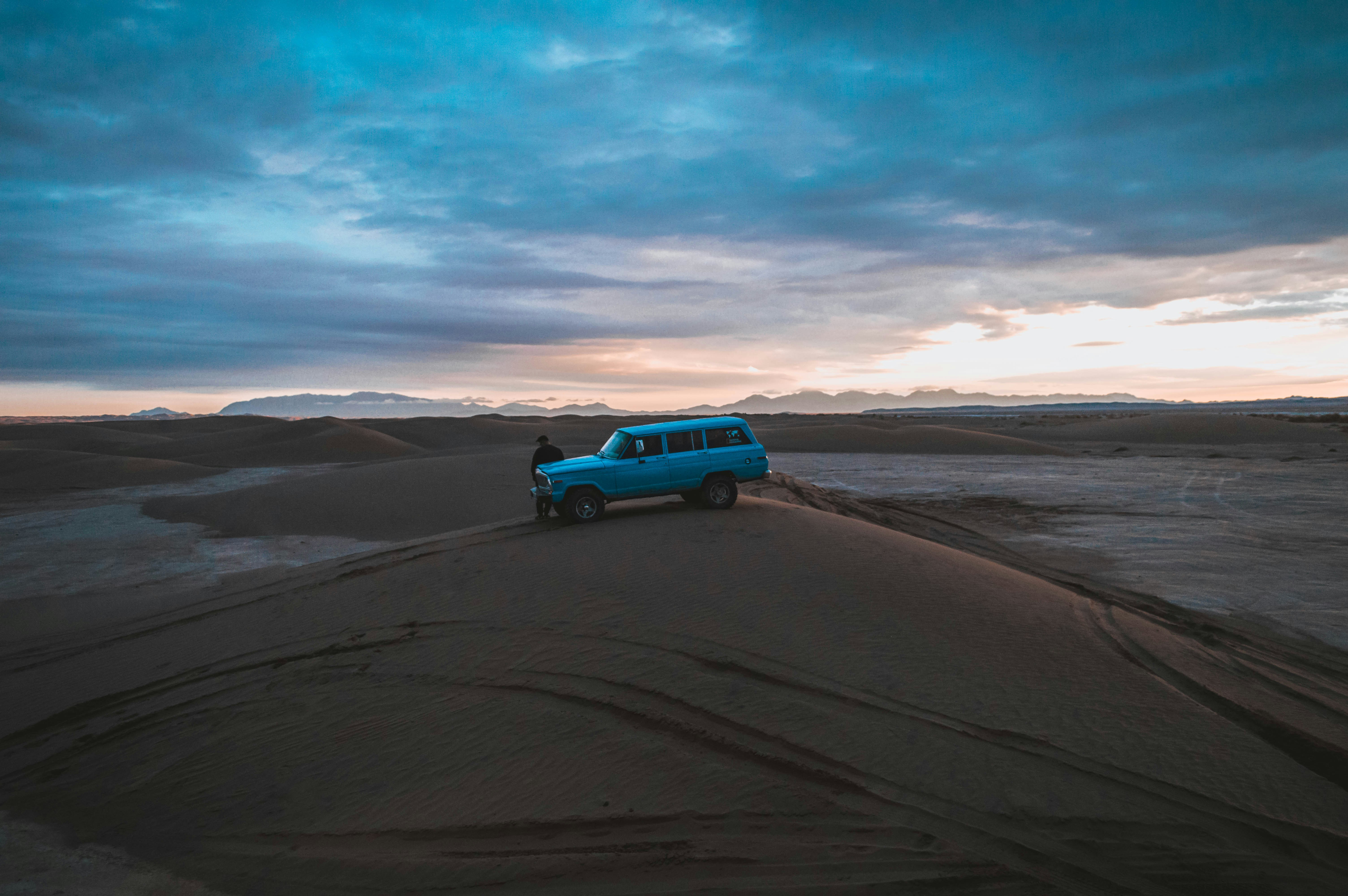Blue SUV carving a wind-sculpted dune under a bruised desert sunset
