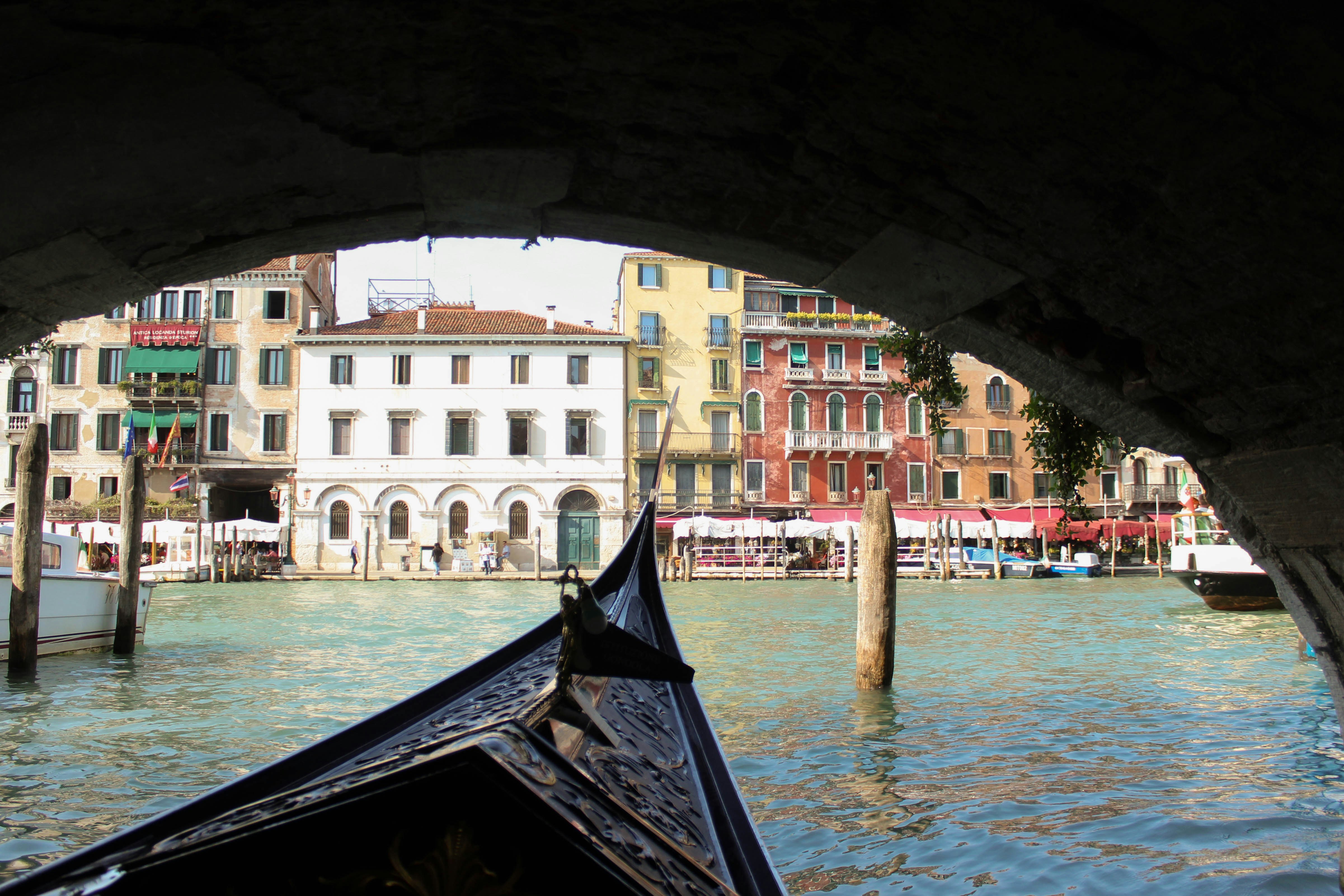 Gondola navigating through an arched stone passage, revealing vibrant Venetian buildings and serene waters beyond.