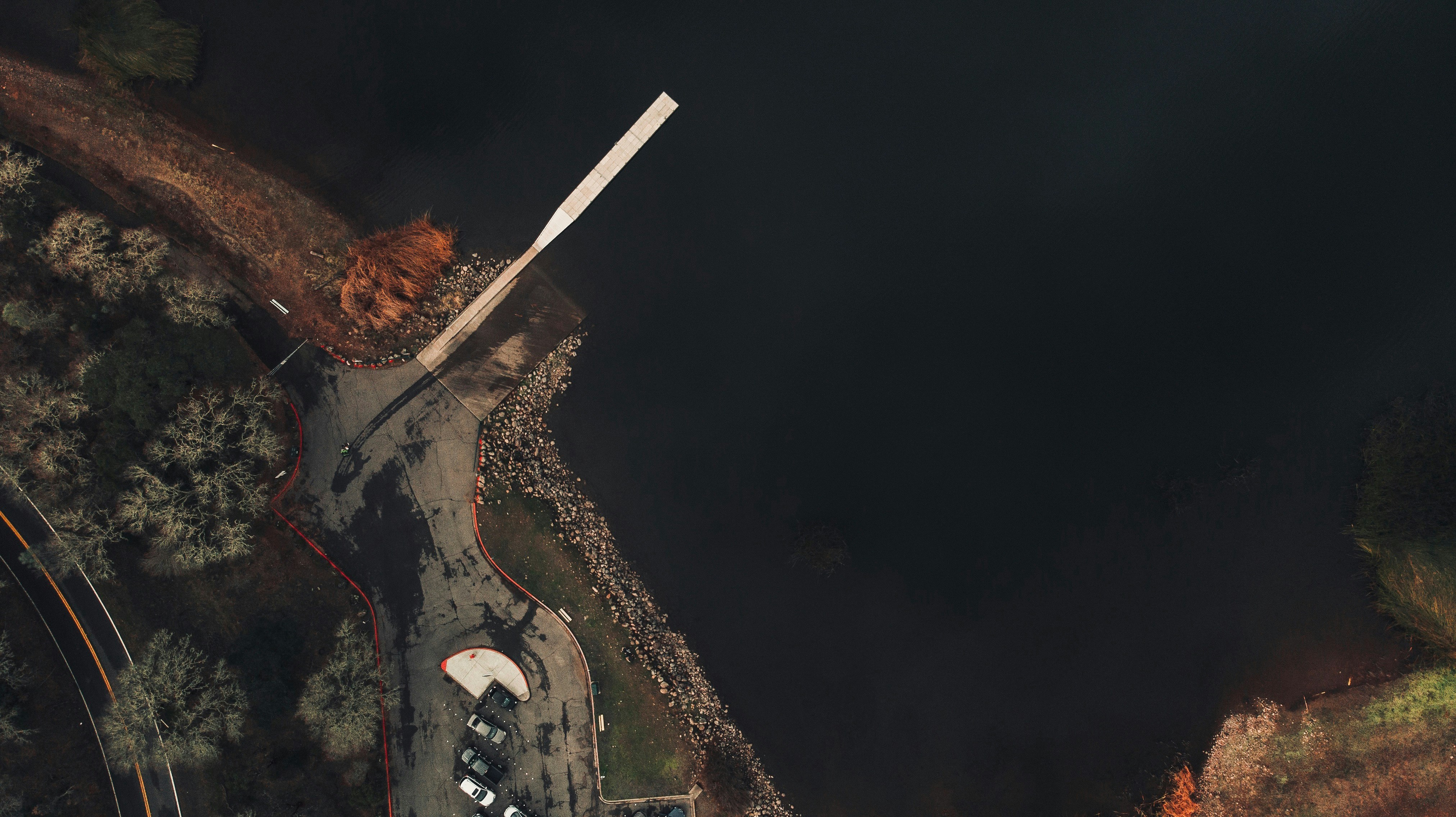 Aerial view of a dock extending into a dark lake, surrounded by trees and a winding road. The scene captures the tranquility of nature at twilight.