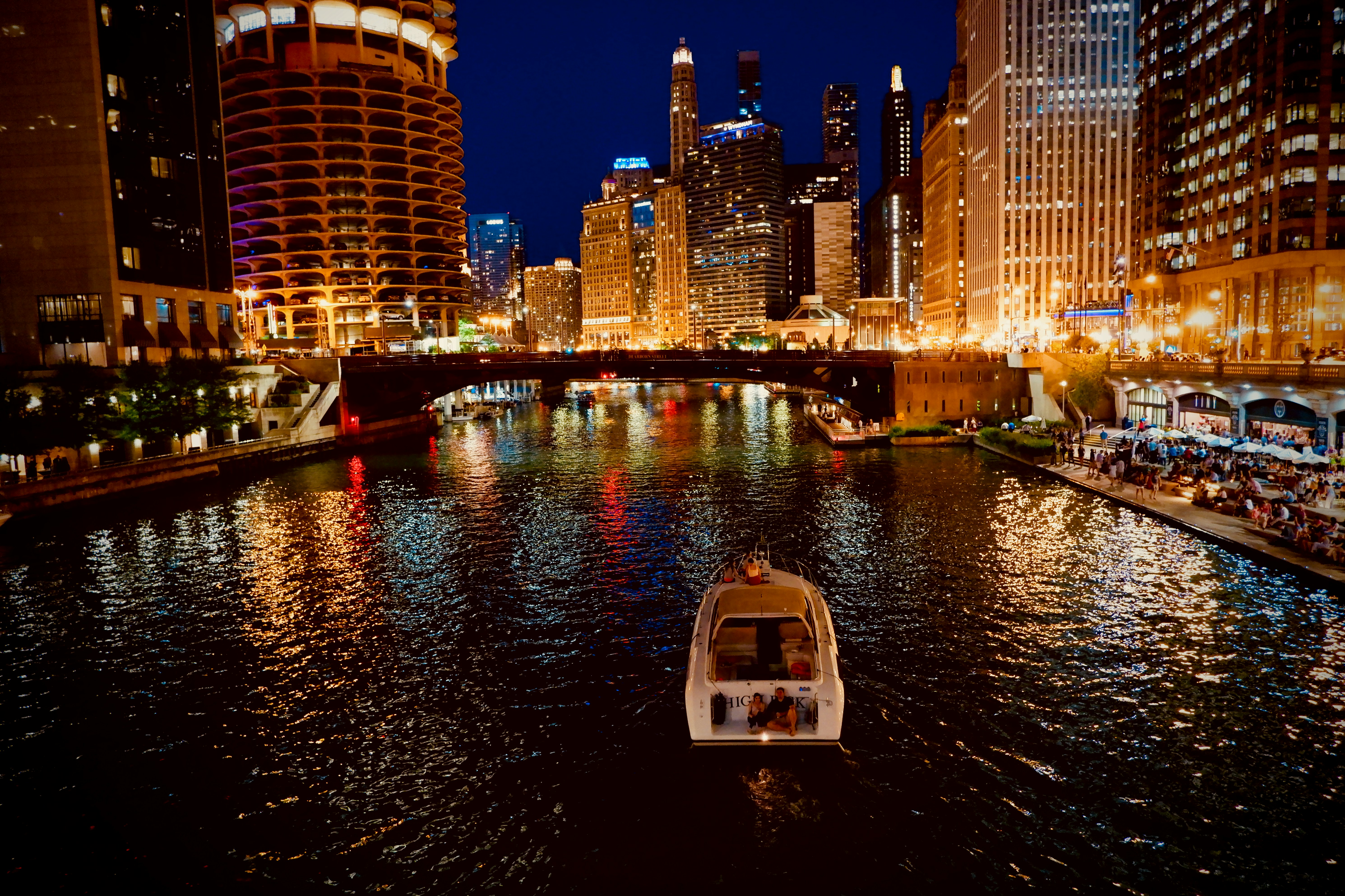A boat glides through the illuminated Chicago River, surrounded by the vibrant skyline and reflections of city lights on the water.