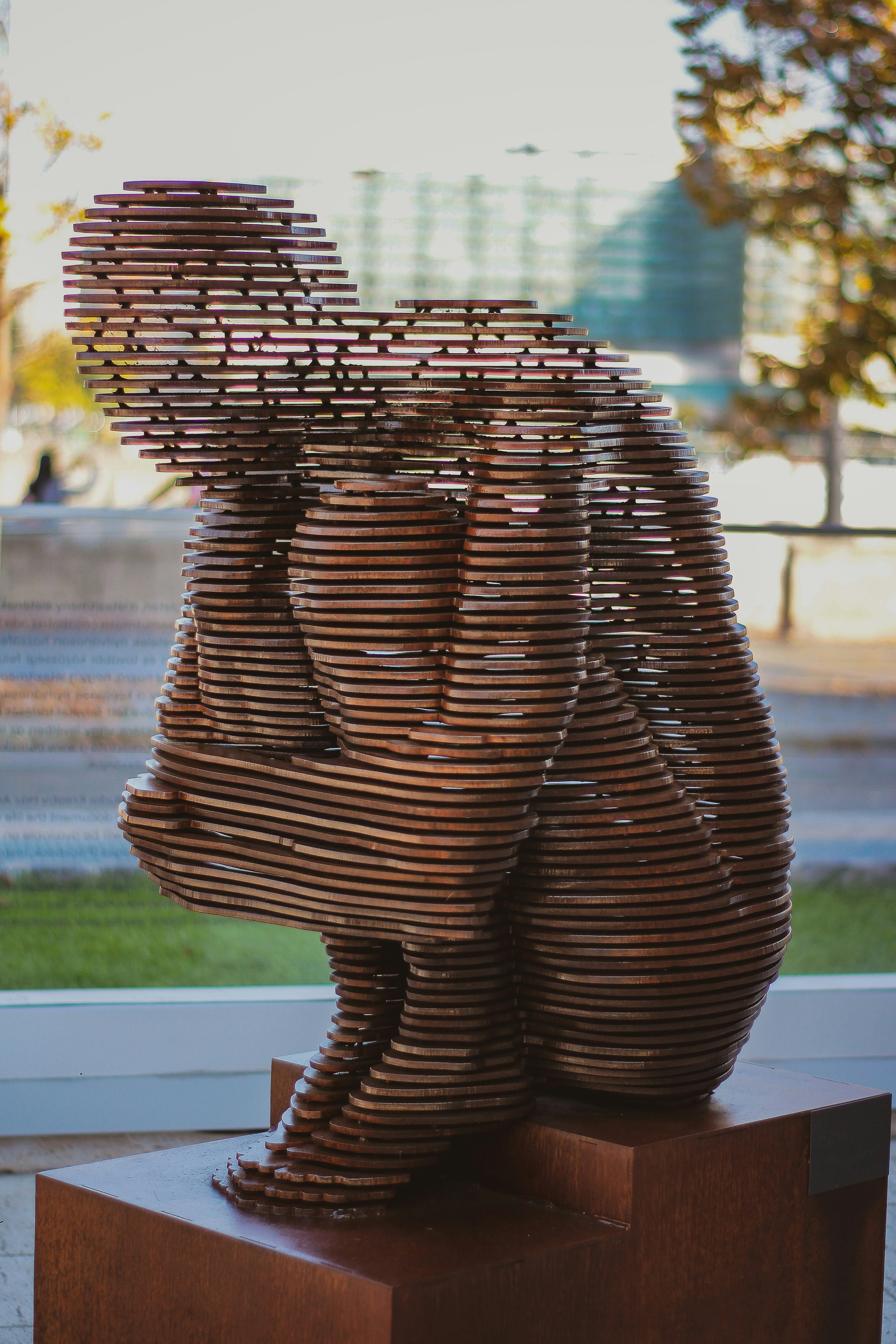Abstract sculpture of a seated figure composed of layered wood strips, conveying a sense of introspection and emotion.