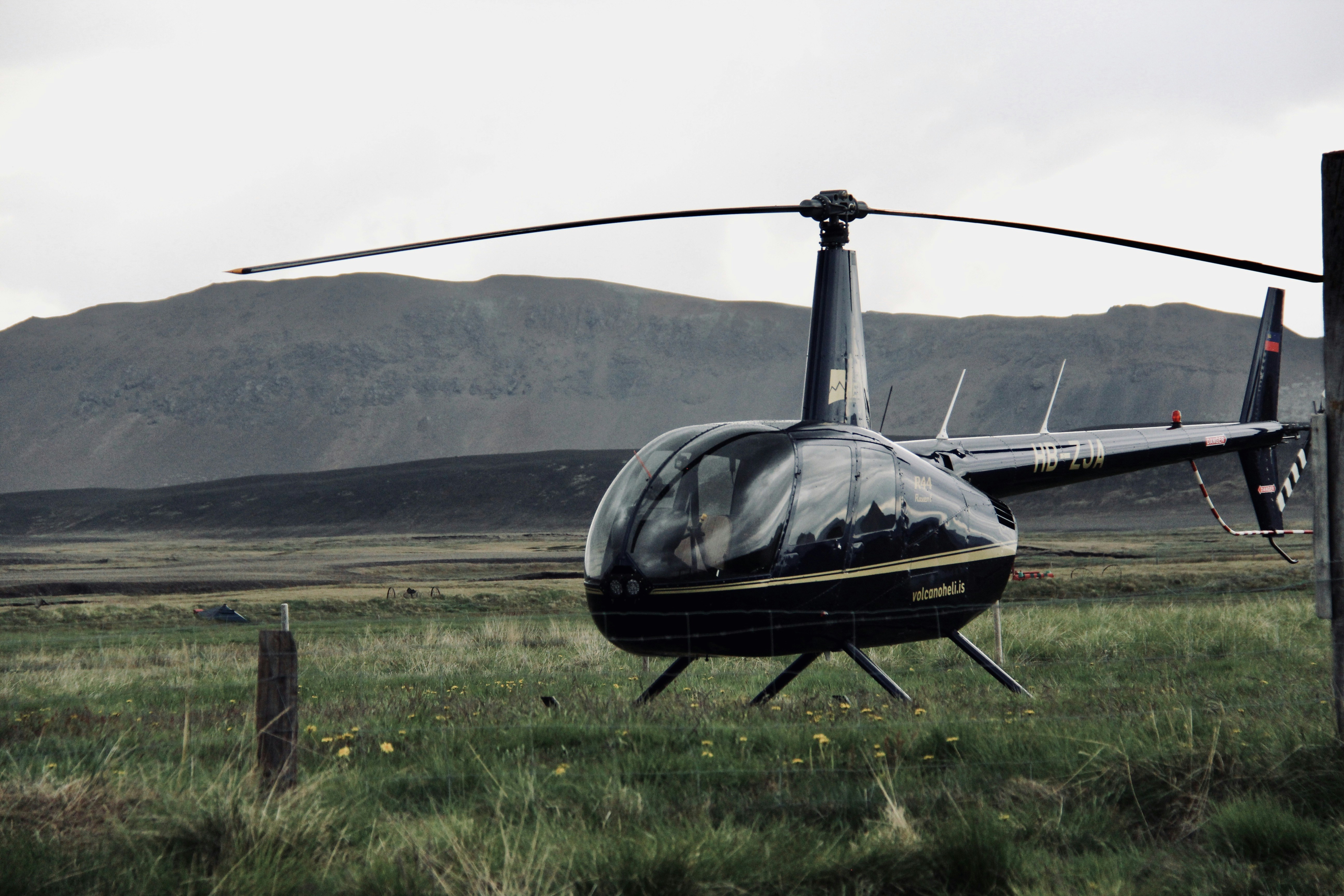 Glossy Black Helicopter Resting in Windswept Grass Before Distant Volcanic Hills