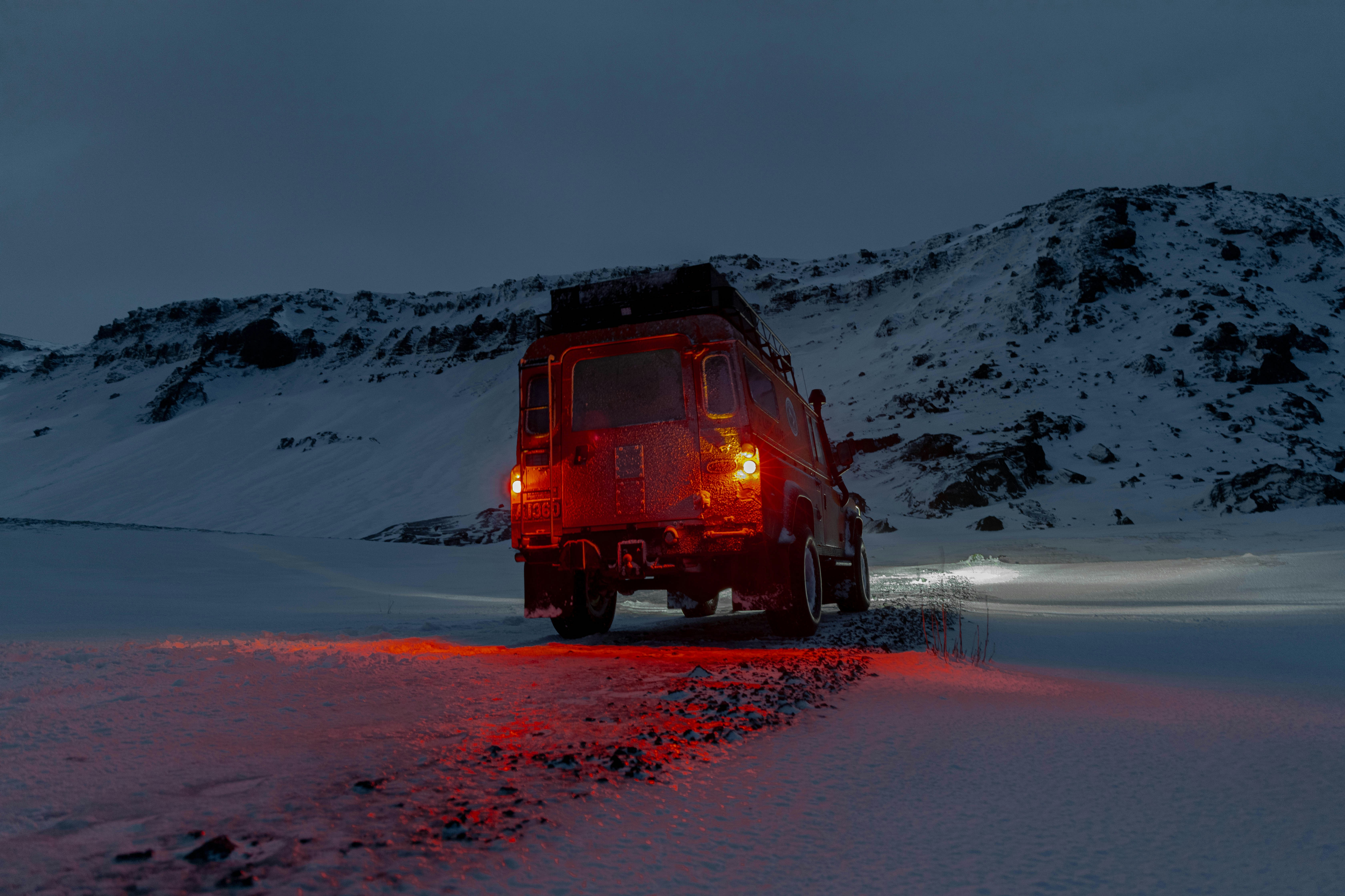 A rugged vehicle navigates a snowy landscape under a twilight sky, illuminated by its rear lights. The scene conveys a sense of adventure and isolation.