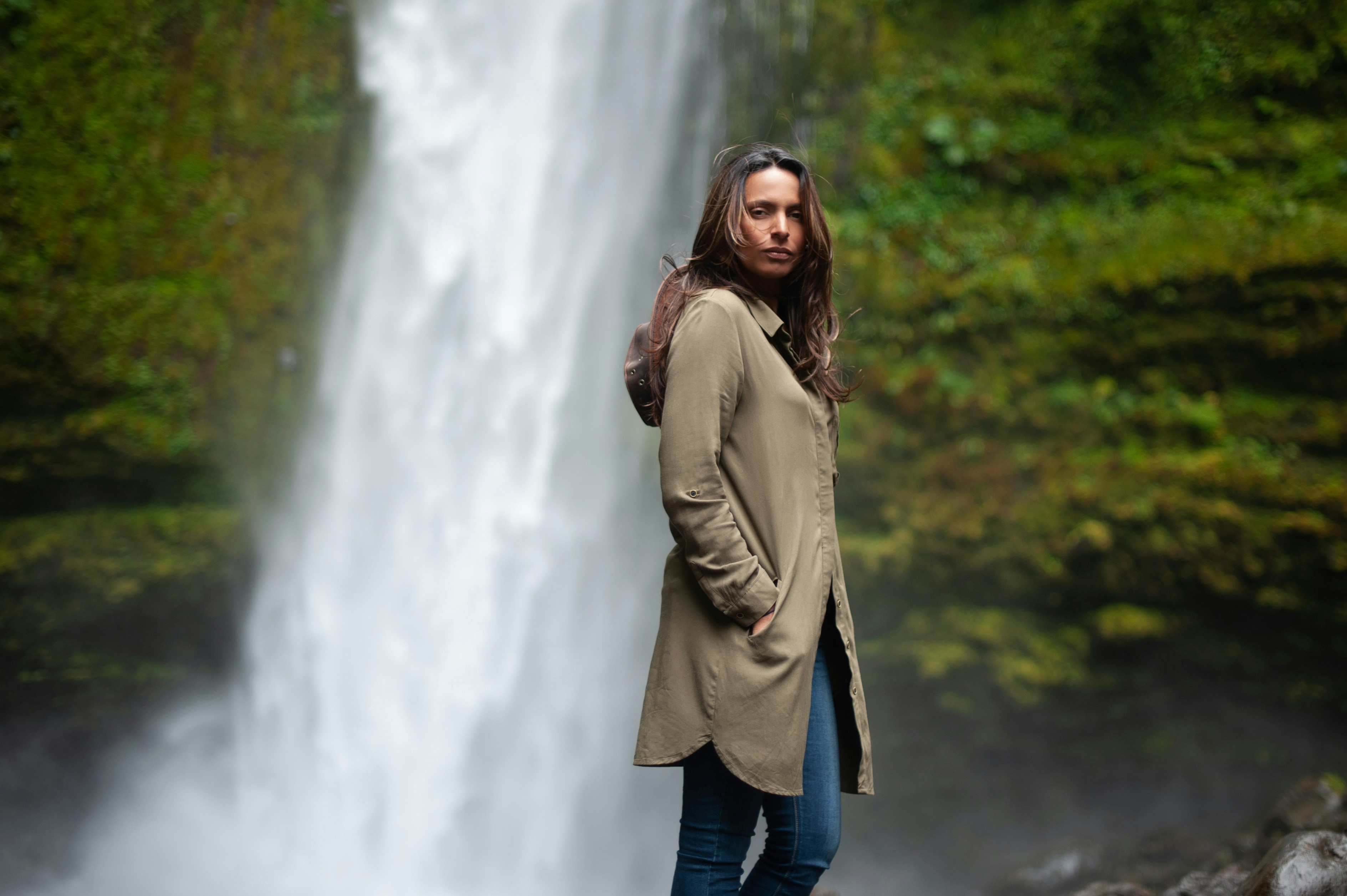 Person standing in front of a cascading waterfall surrounded by lush greenery.