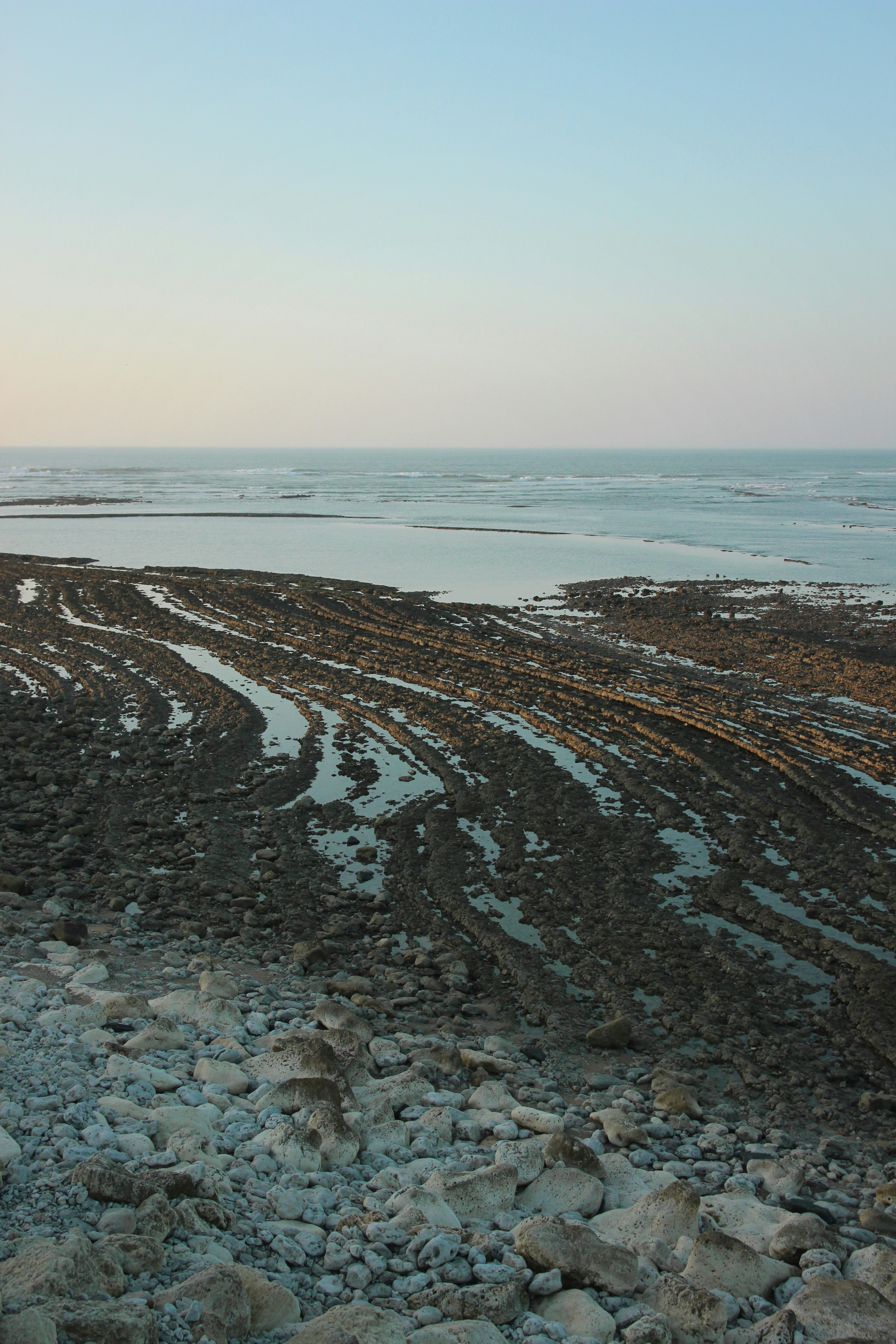 Intricate tidal patterns etched into rocky shoreline at low tide, revealing a serene coastal landscape.