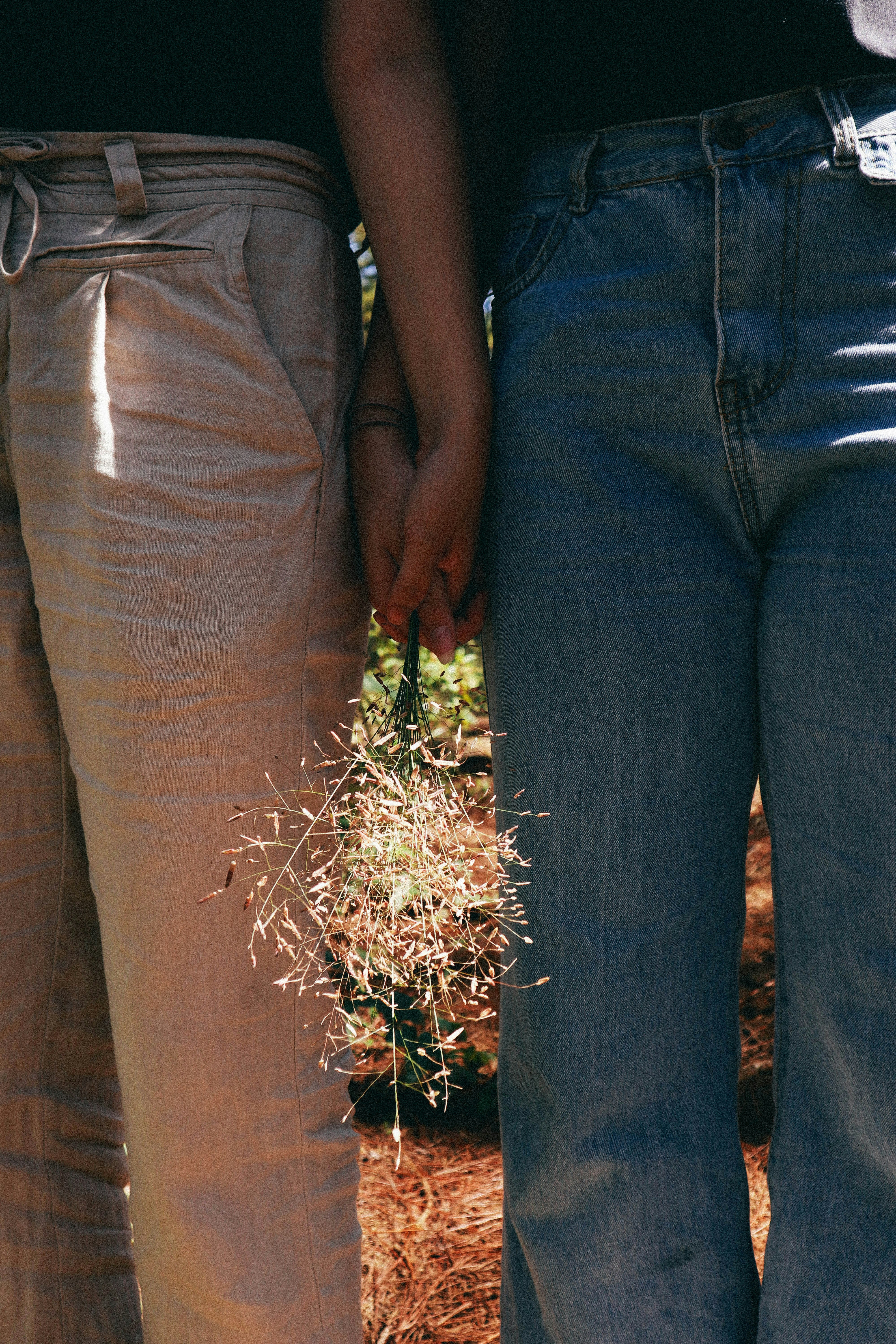 Two individuals holding hands, with a bouquet of wildflowers in the foreground, surrounded by lush greenery.
