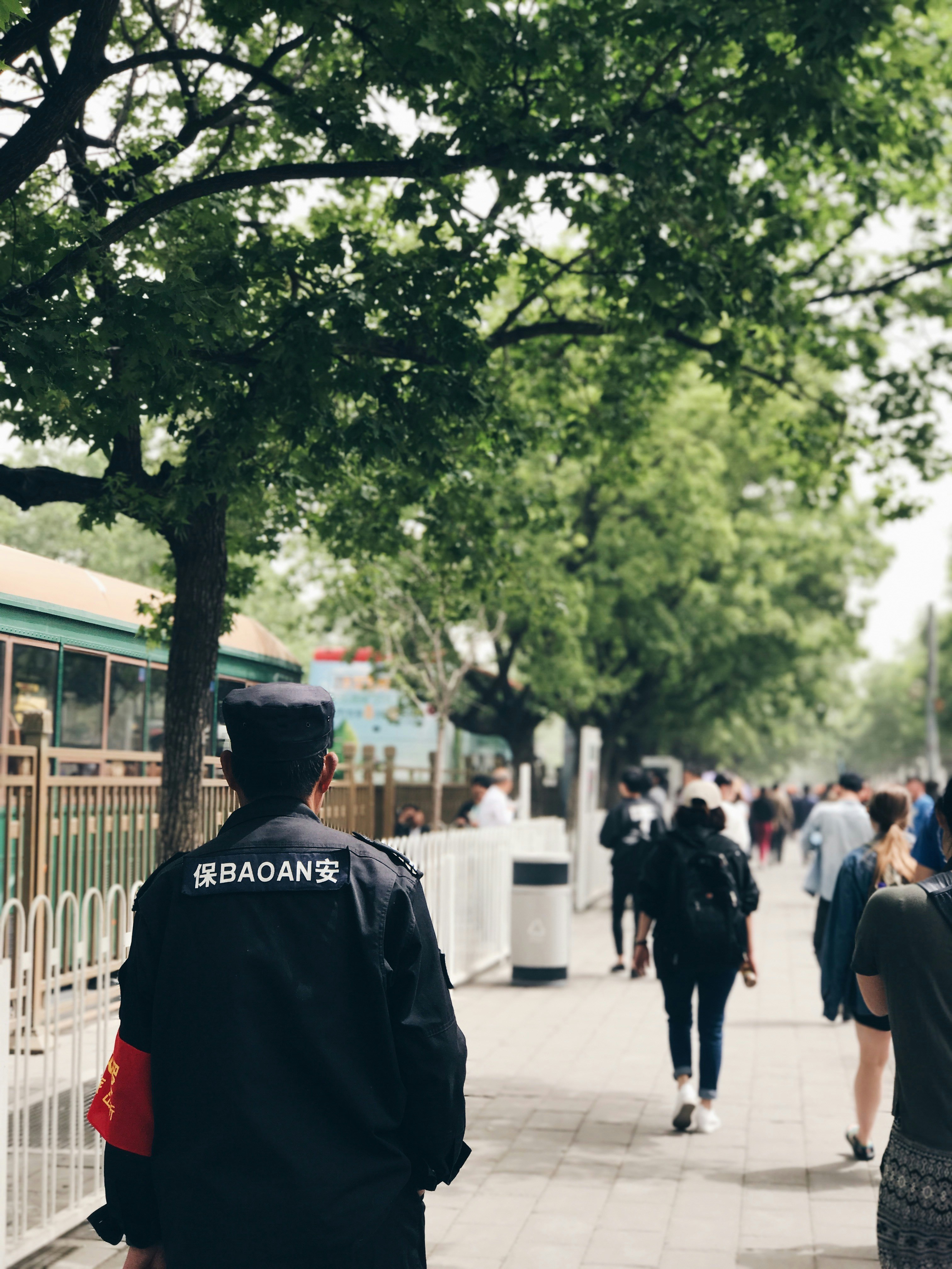 Security personnel monitoring a busy street lined with trees and pedestrians, capturing the essence of urban life and safety.