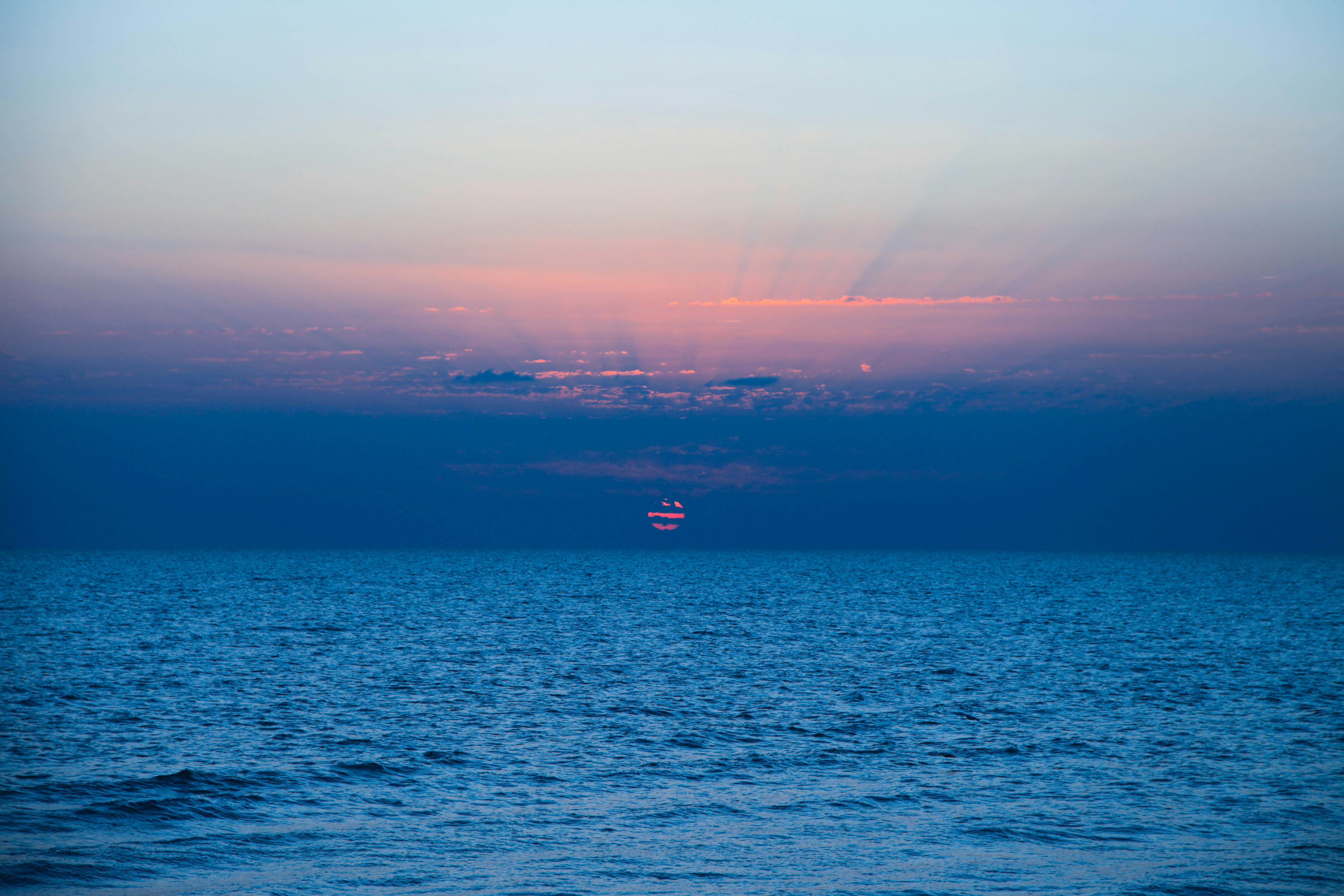 Sunset over a calm ocean with a gradient sky transitioning from pink to blue.