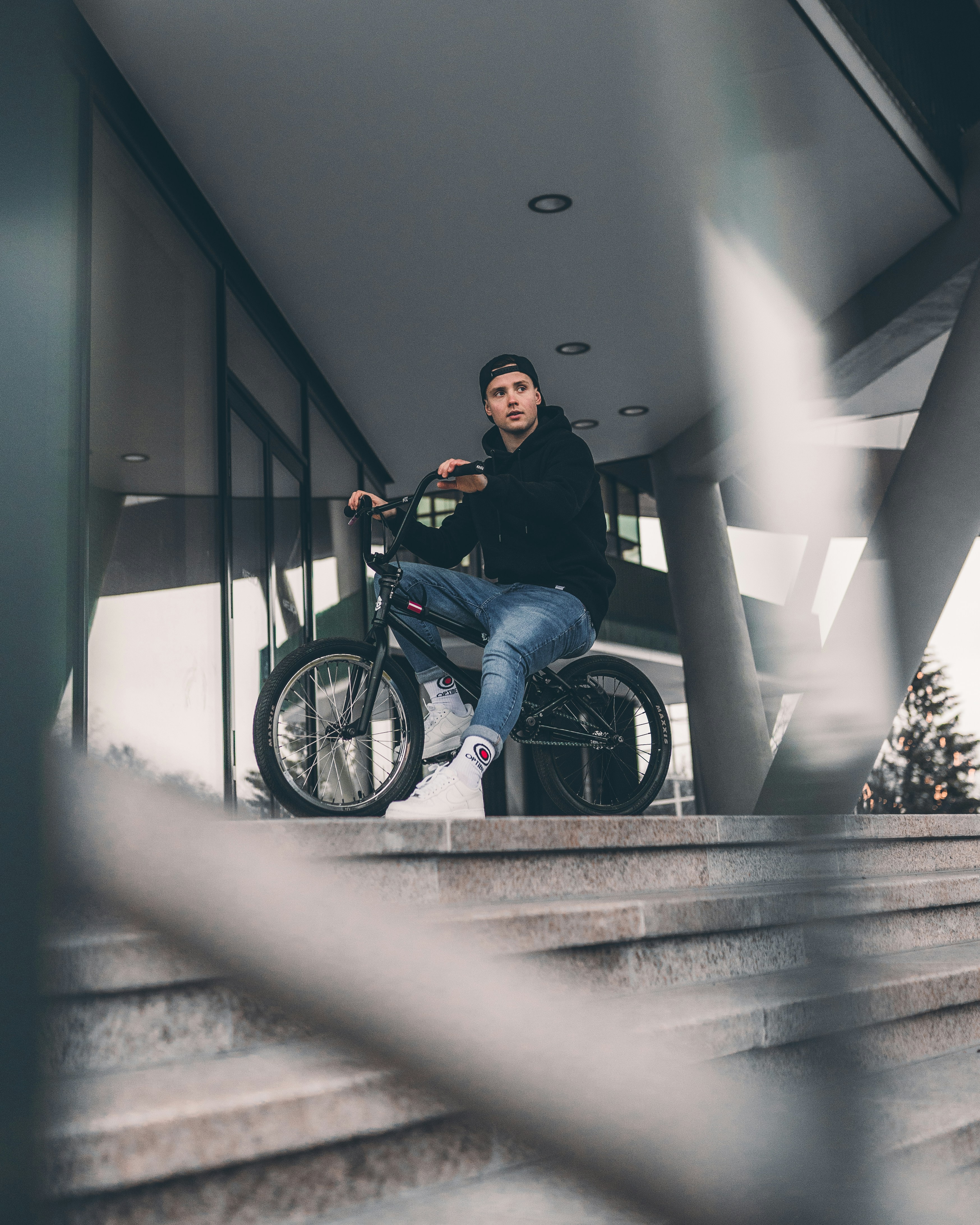BMX rider seated on his bike atop city steps, framed by modern architecture.
