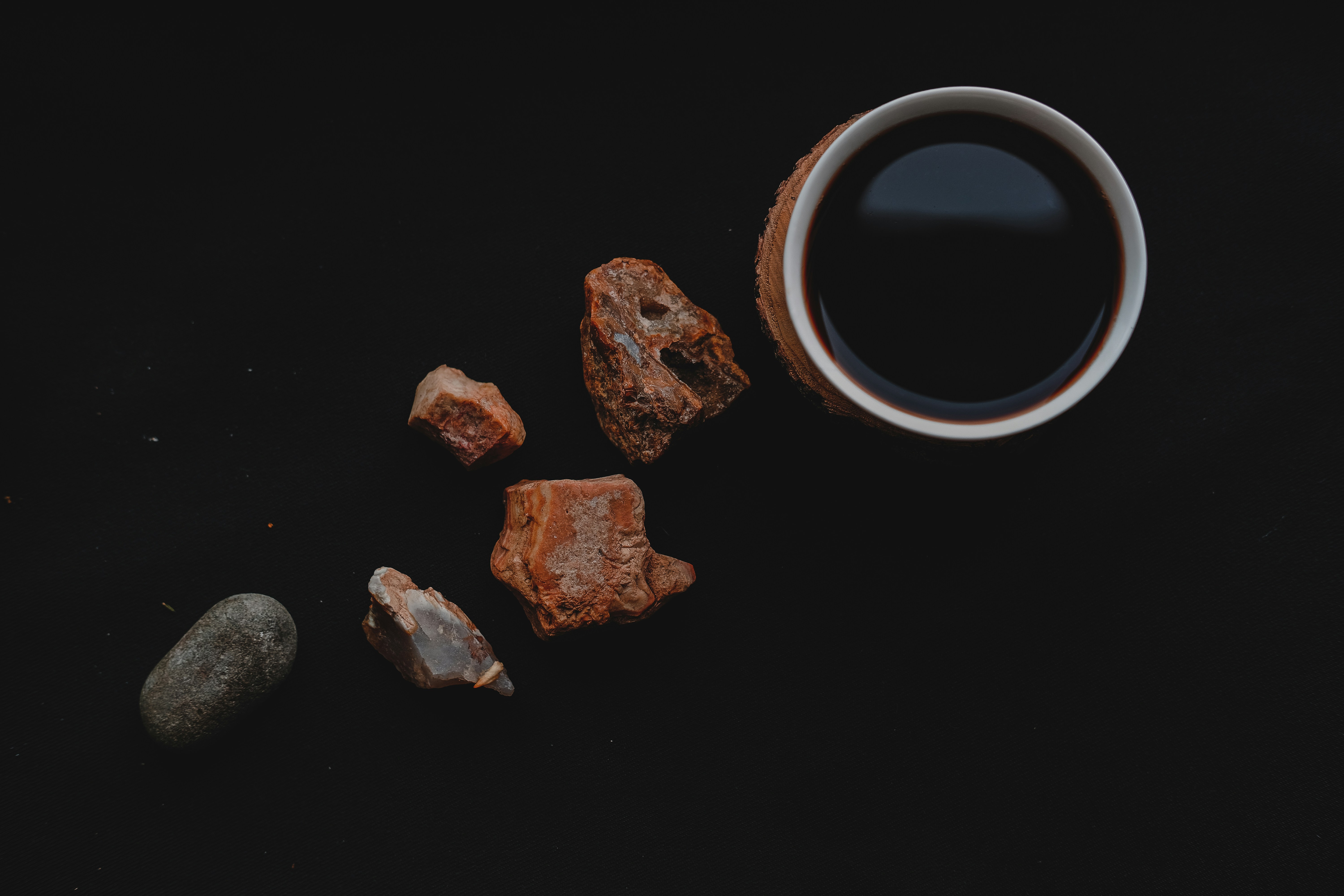 Noir Still Life: A Ceramic Cup and Pebbles on Velvet Darkness