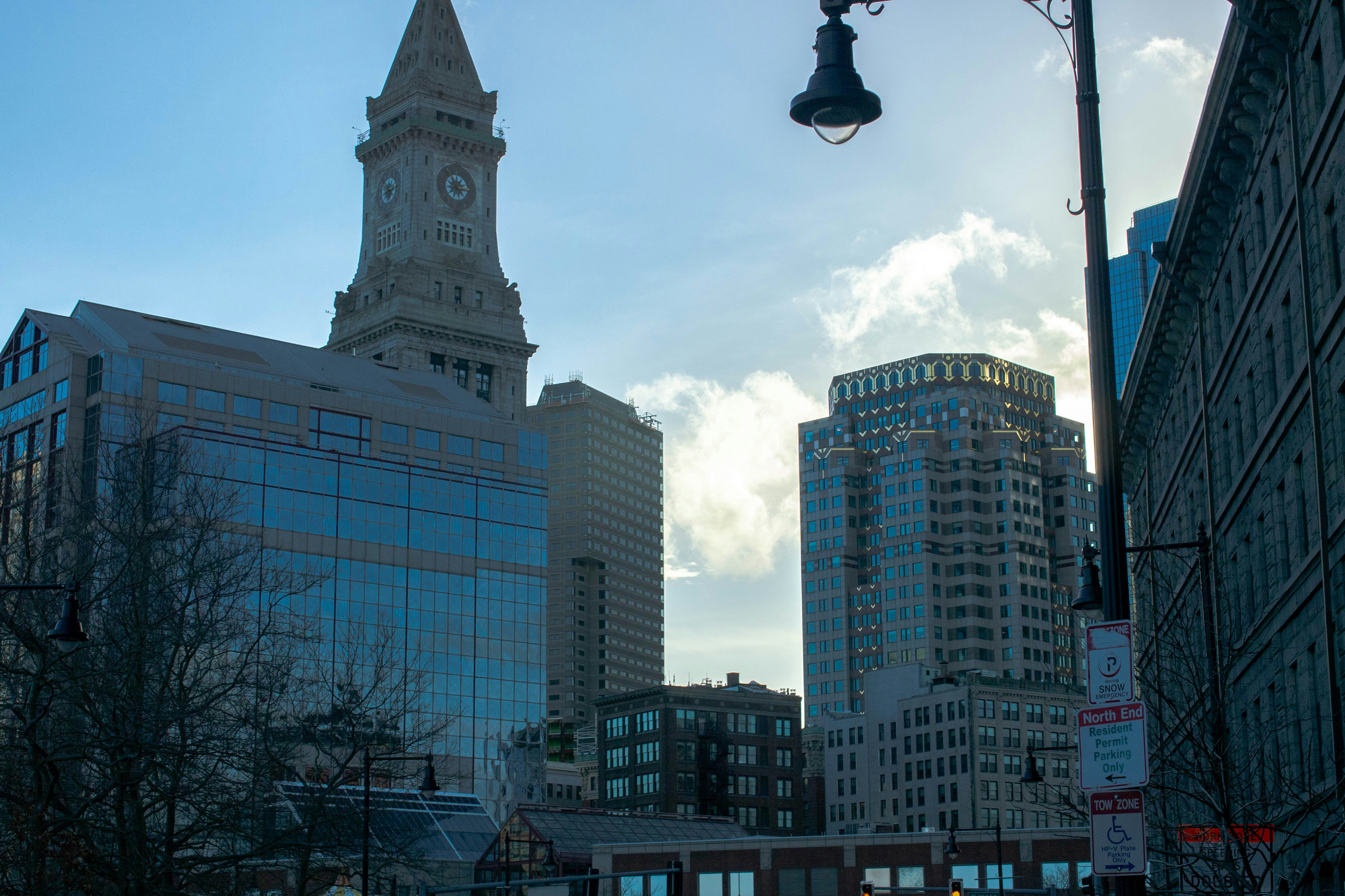 Sculpted cityscape with a prominent clocktower and surrounding high-rises under bright winter daylight. A street scene with bare trees and a foreground urban edge framing the skyline.