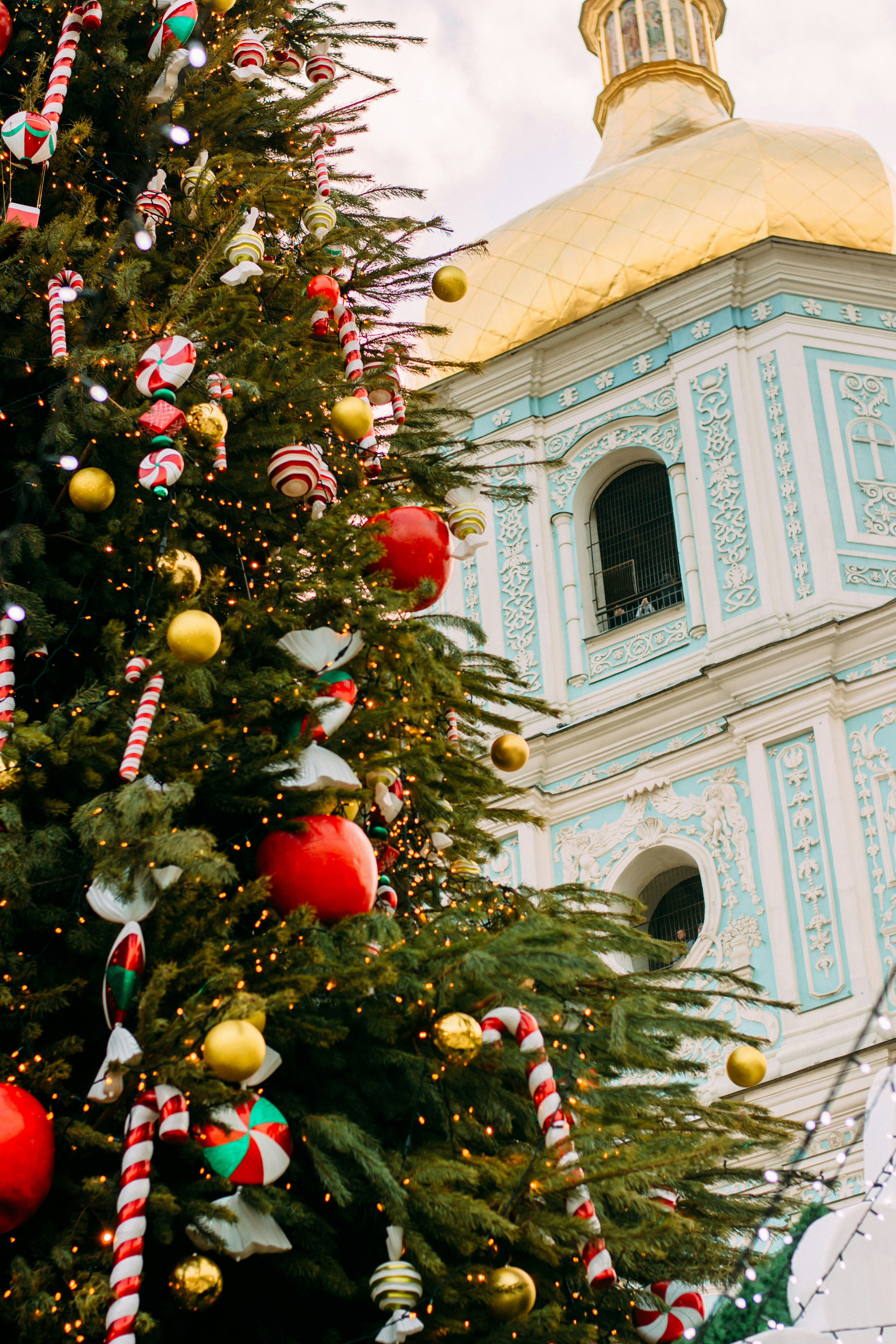 Decorated Christmas tree adorned with colorful ornaments and lights, juxtaposed against an ornate blue and gold church facade.