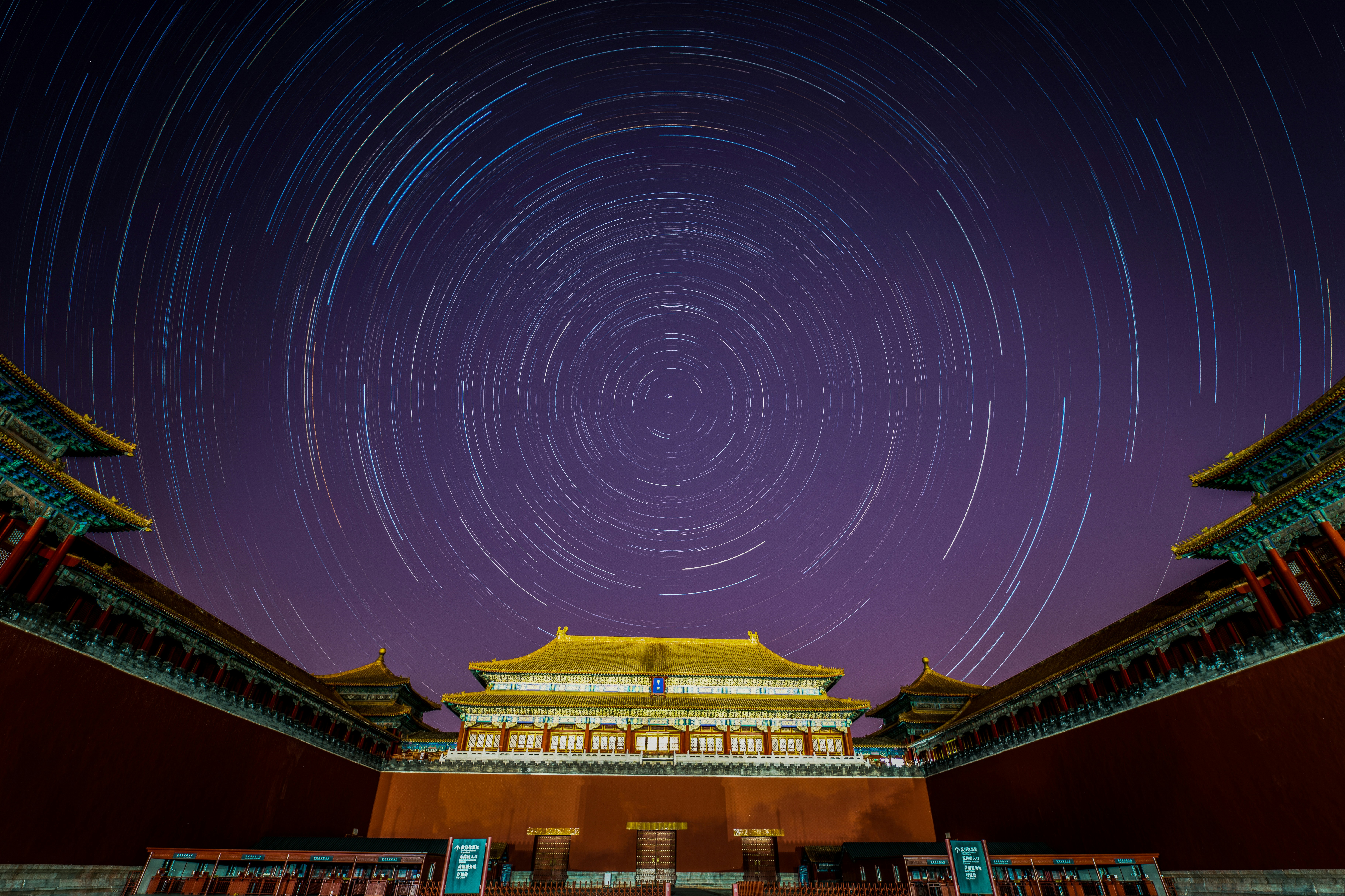 Long-exposure photograph shows star trails circling the night sky above the Forbidden City’s central pavilion, framed by glowing red walls.