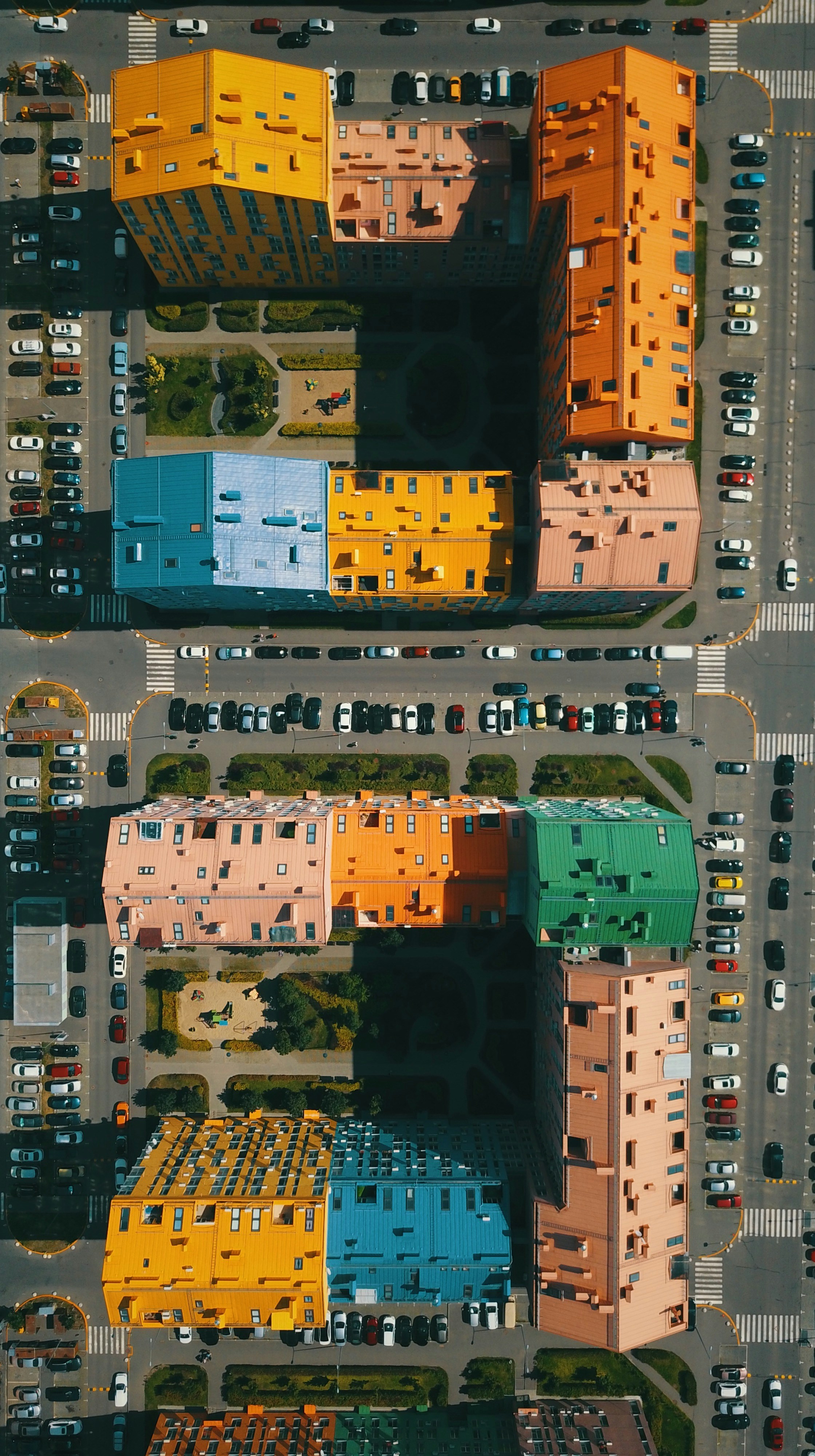 Vibrant rooftops of residential buildings arranged in a geometric pattern, surrounded by a parking lot. The scene showcases a blend of colors and shapes.