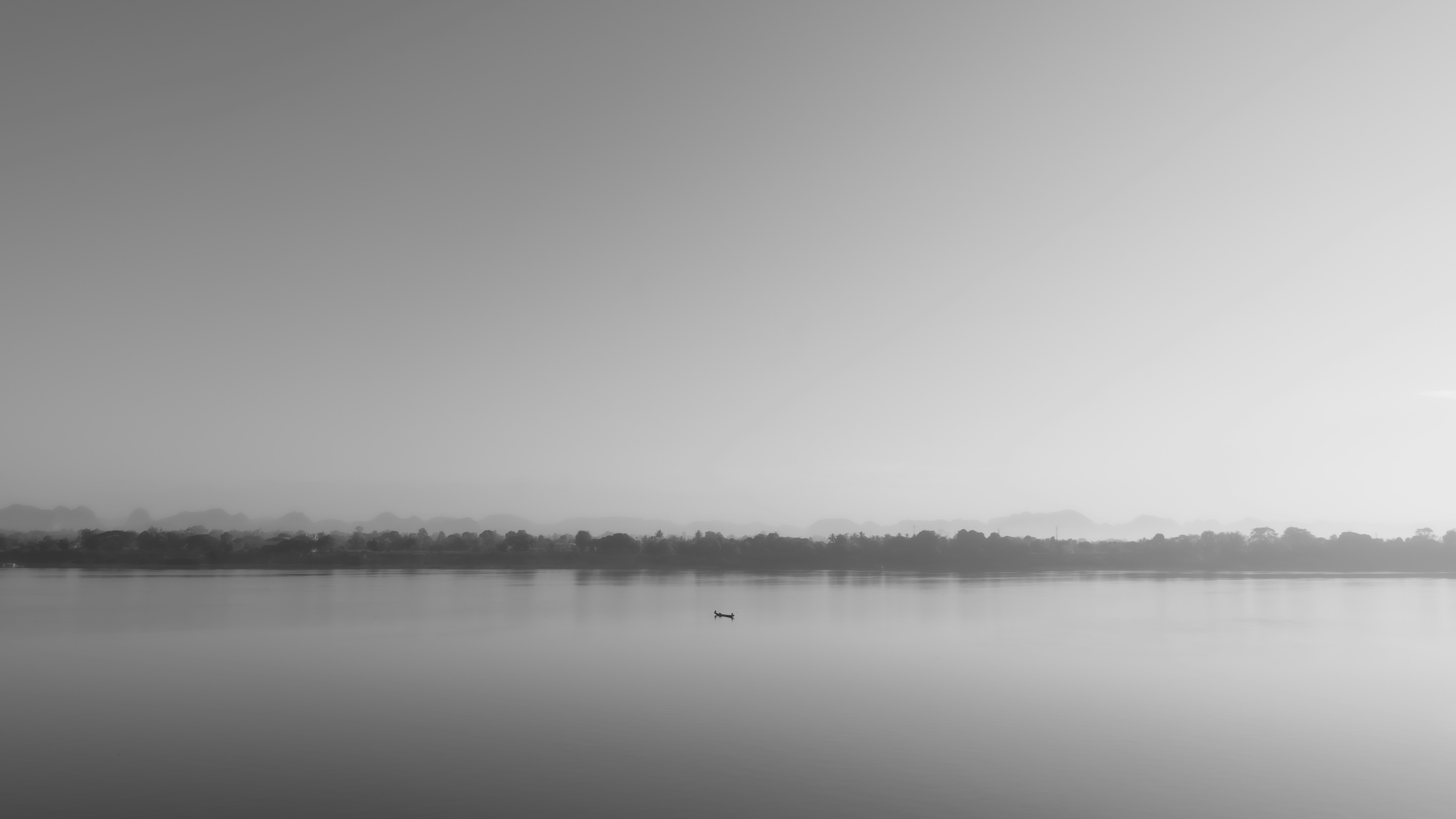 Small boat floats peacefully on a vast, calm lake under a clear sky.