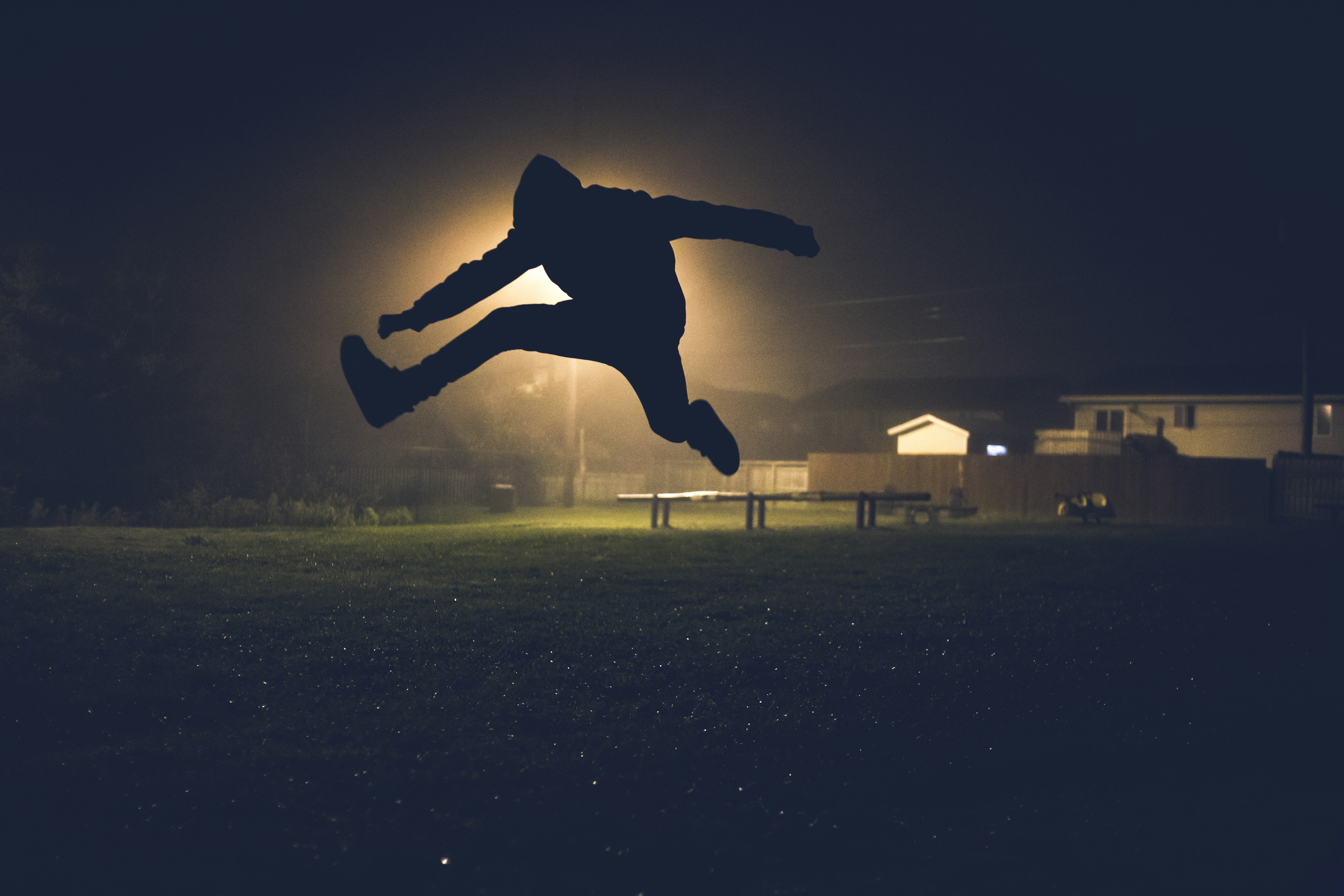 Nighttime silhouette of a high leap over an illuminated field