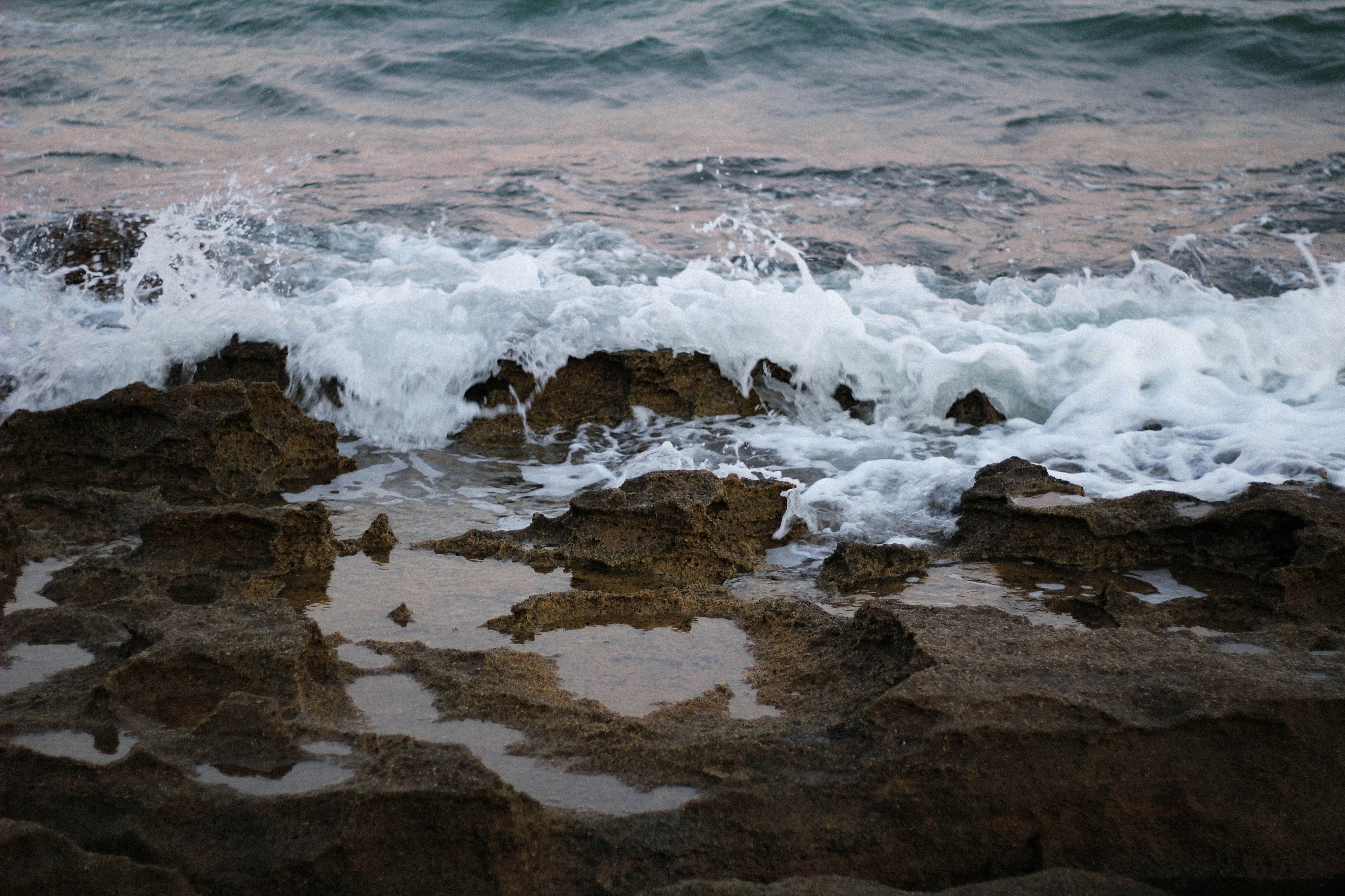 Foamy waves crashing against rugged rocks at dusk, creating a dynamic interplay of water and stone.
