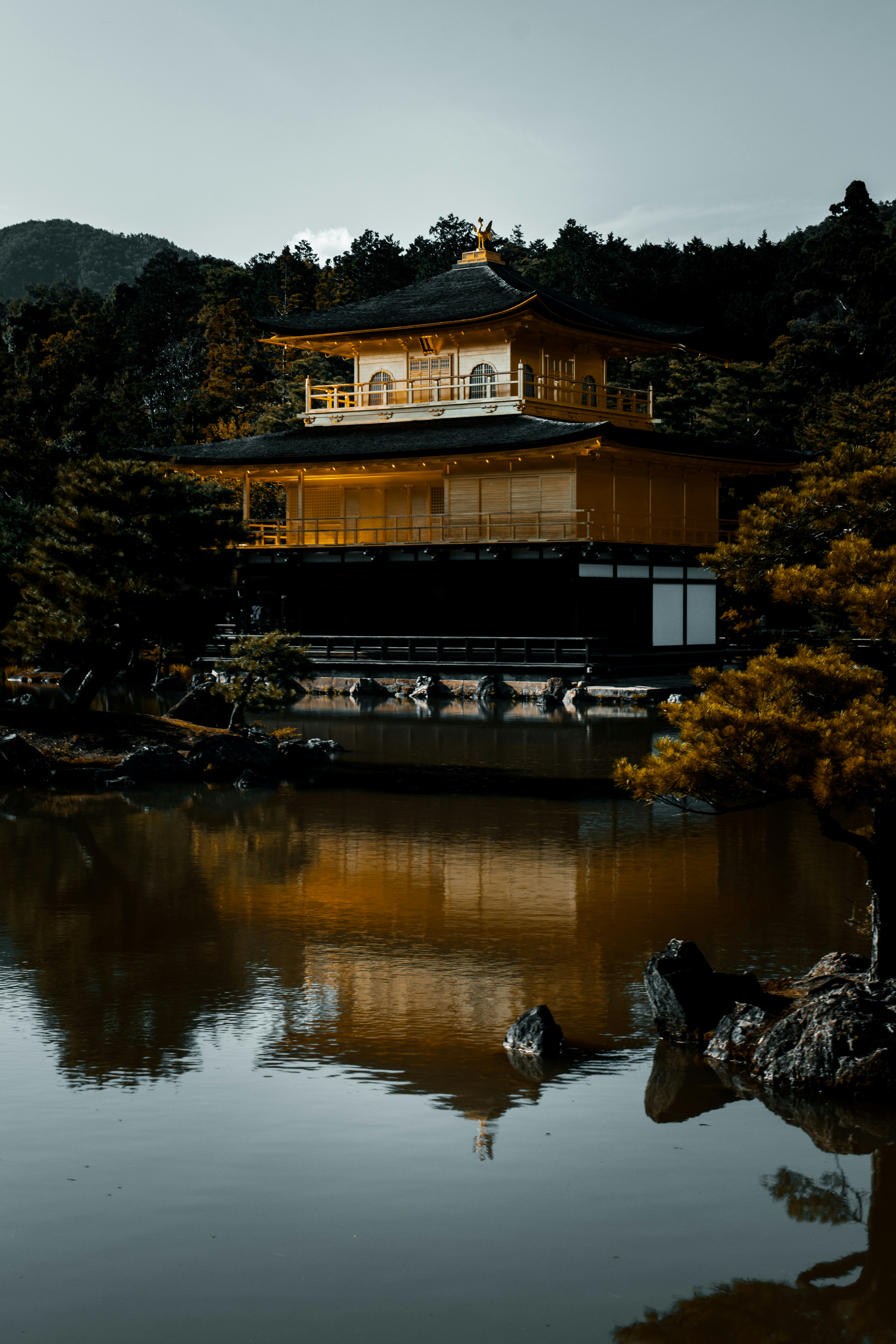 Golden pavilion surrounded by tranquil waters and lush greenery, reflecting its beauty on the surface. The scene captures a moment of peace in a historic setting.
