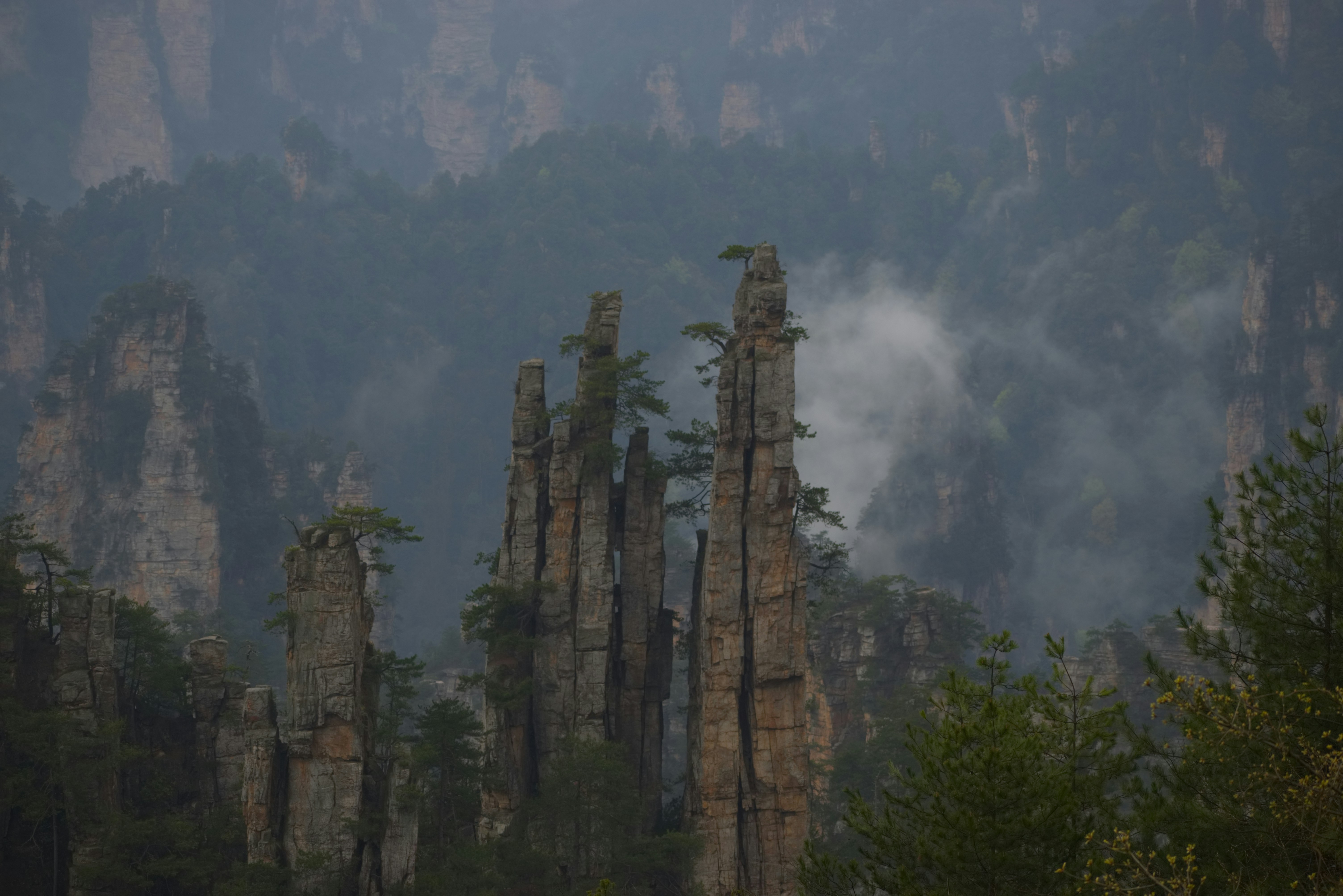 Towering rock formations rise amidst a misty landscape, shrouded in mystery and enveloped by lush greenery.