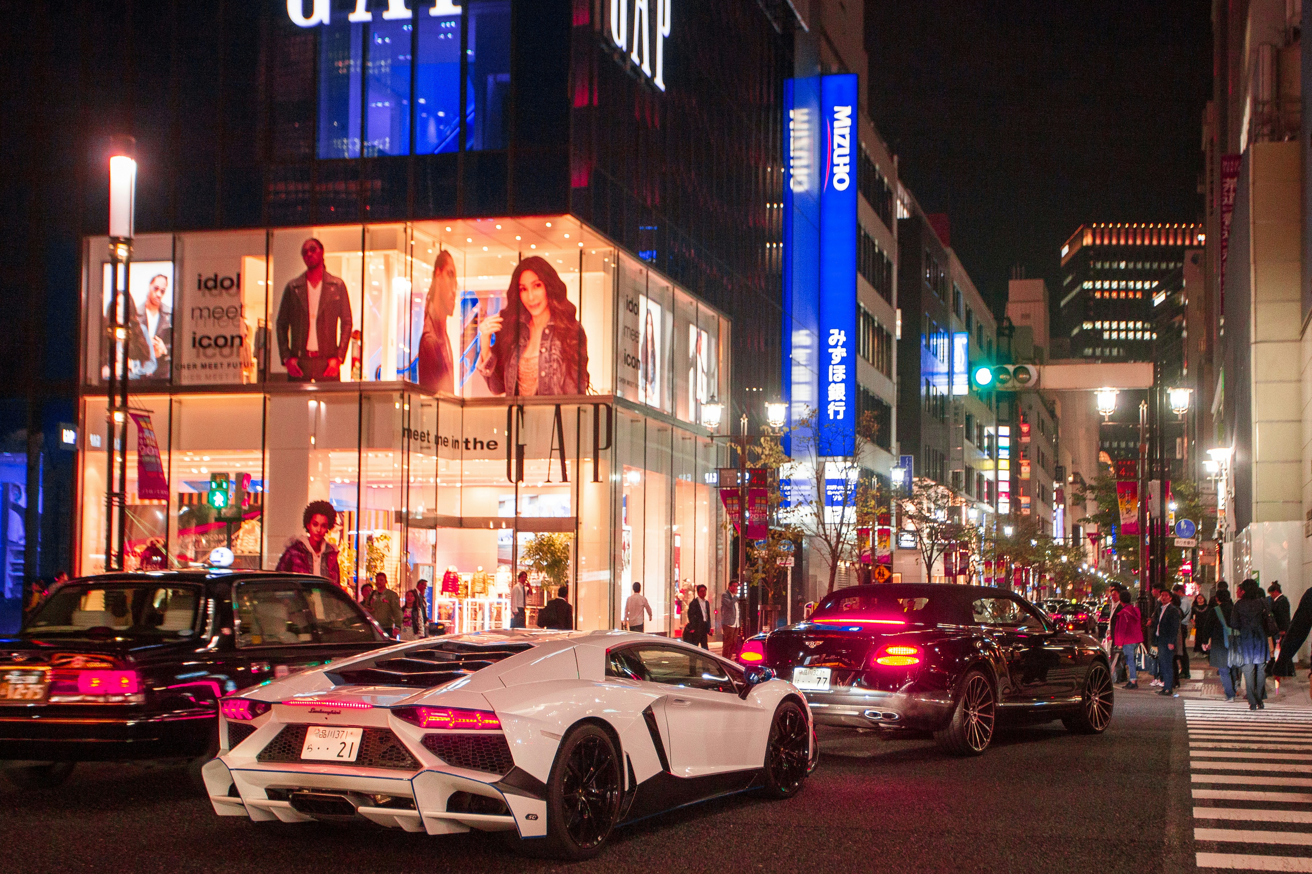 Luxury cars navigate the vibrant, illuminated streets of Ginza, Tokyo at night.